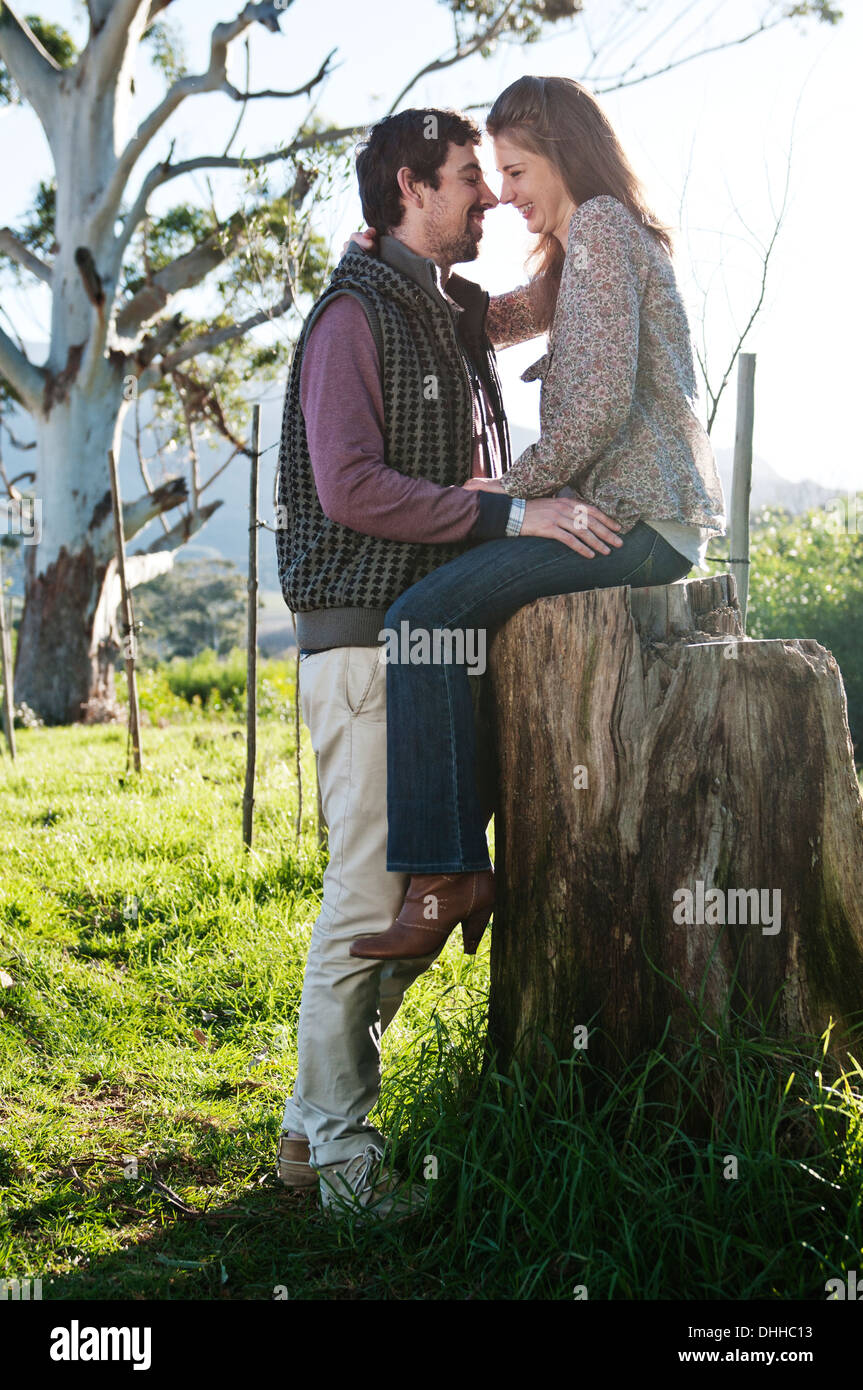 Young woman sitting on tree stump, boyfriend standing in front Stock ...