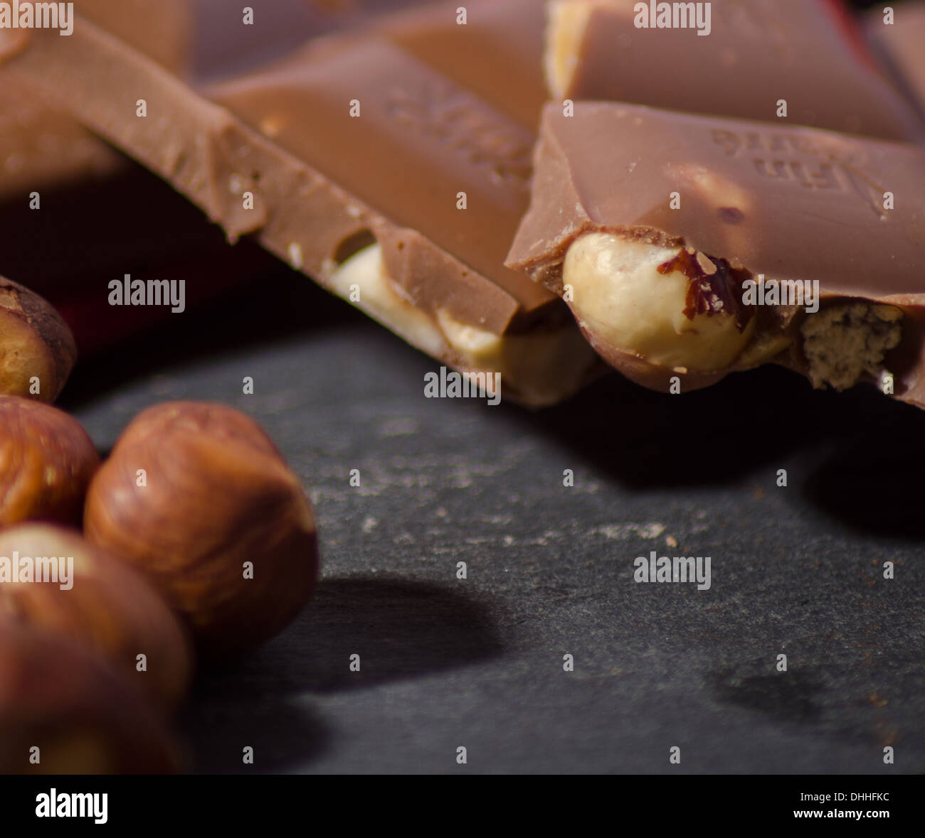 Broken hazelnut chocolate pieces and fresh hazelnuts on grey slate ...