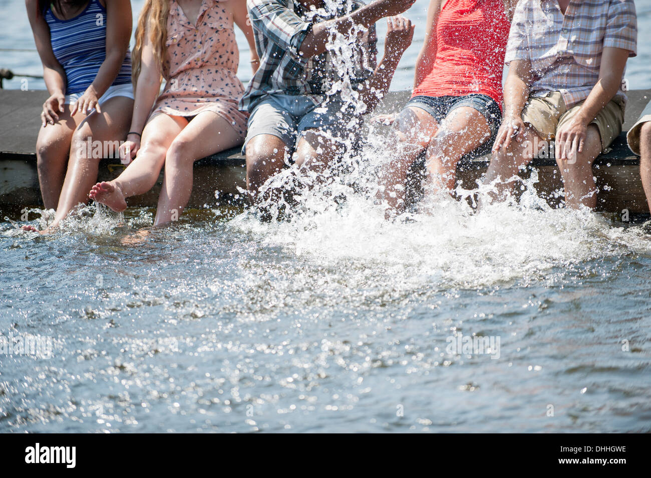 Friends sitting on jetty splashing in lake Stock Photo - Alamy