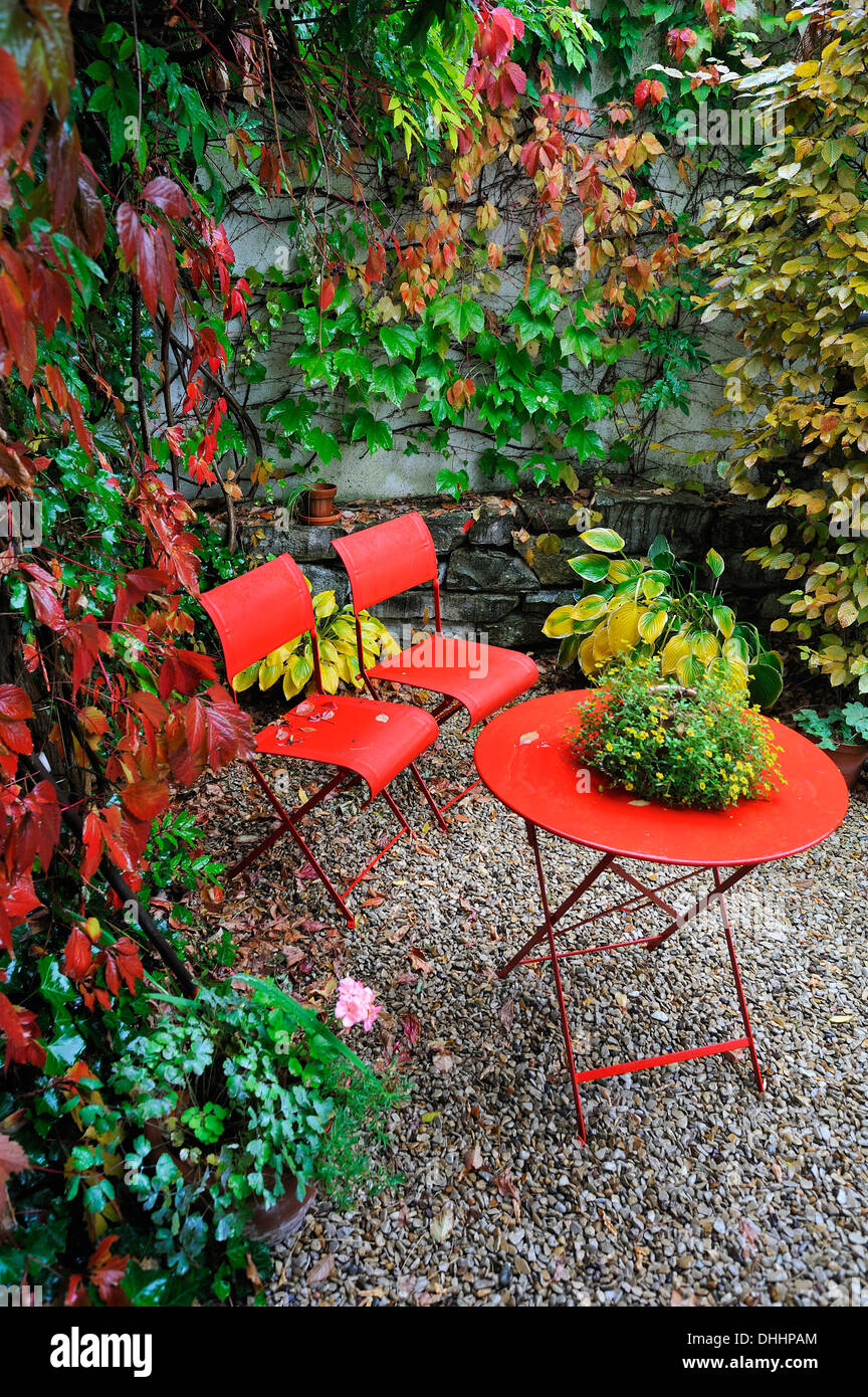 Red garden chairs and table in the rain in an autumn garden corner ...