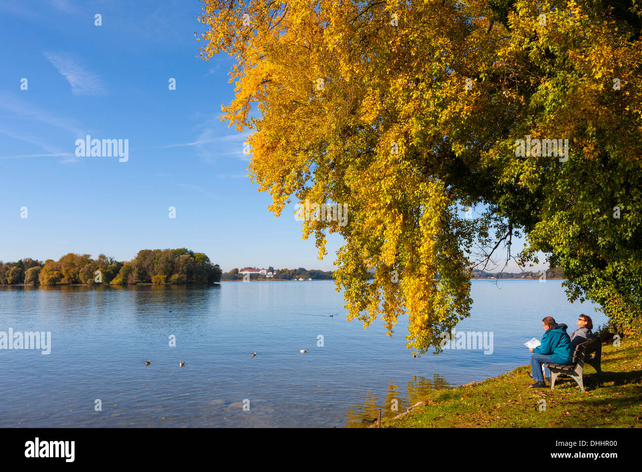 Tourists sitting on a bench at Lake Chiemsee, Island Frauenchiemsee or Fraueninsel, Chiemsee ...