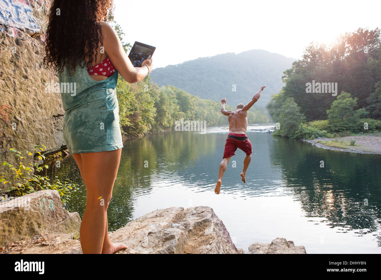 Woman photographing boyfriend jumping from rock ledge, Hamburg ...