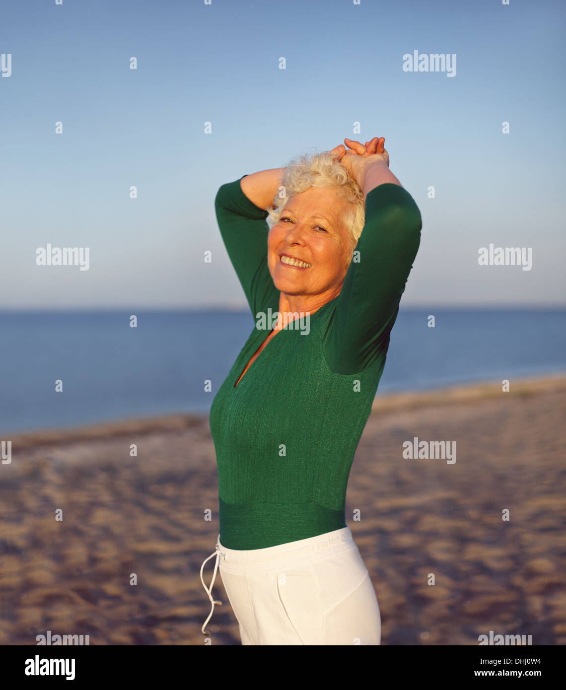 Happy elder woman looking relaxed on the beach with her hands on her ...