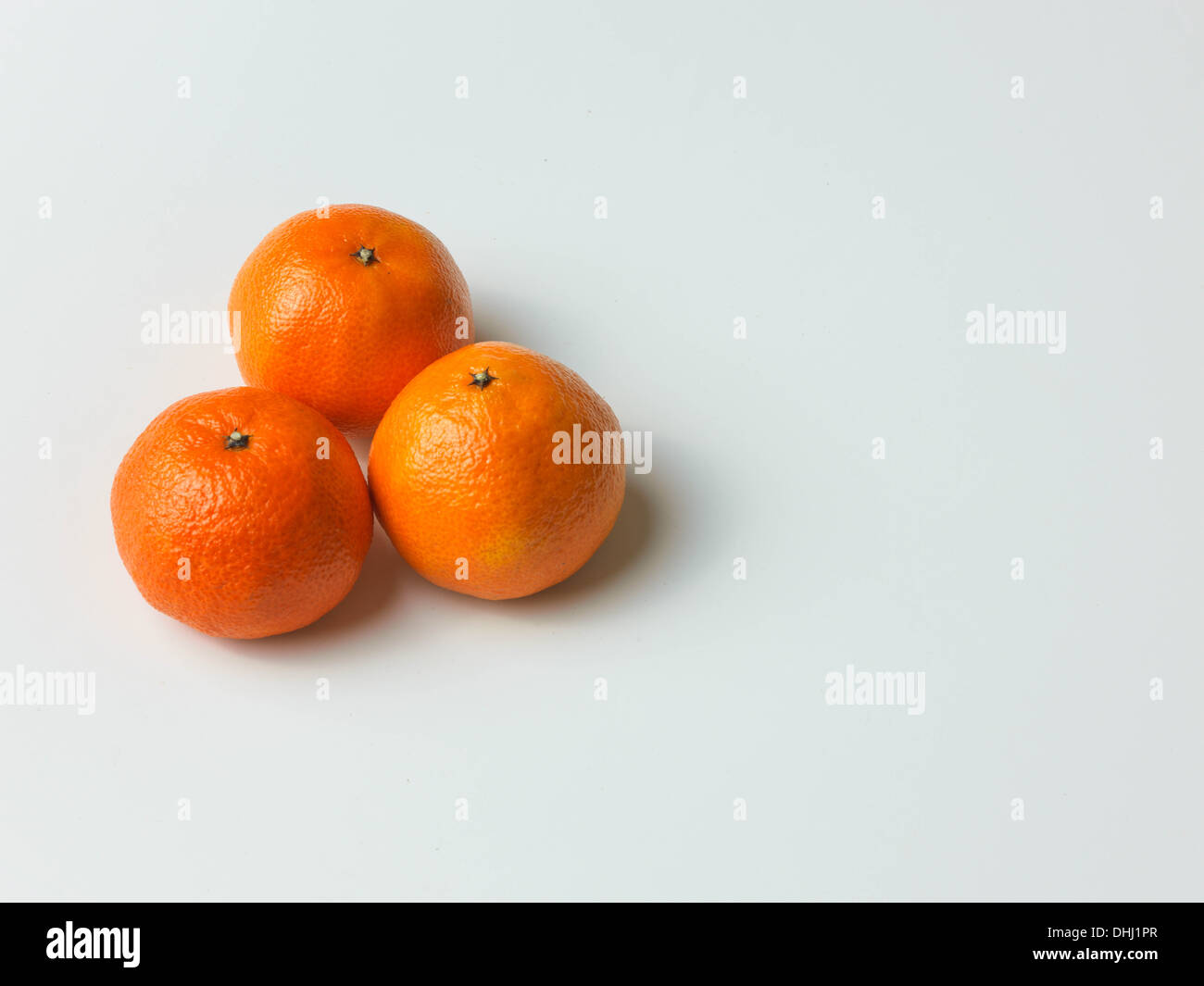 Three orange Clementine arranged in a triangle sit on a white ...