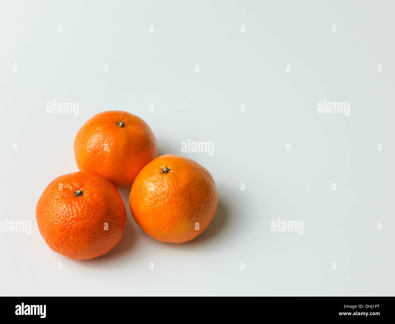 Three orange Clementine arranged in a triangle sit on a white ...
