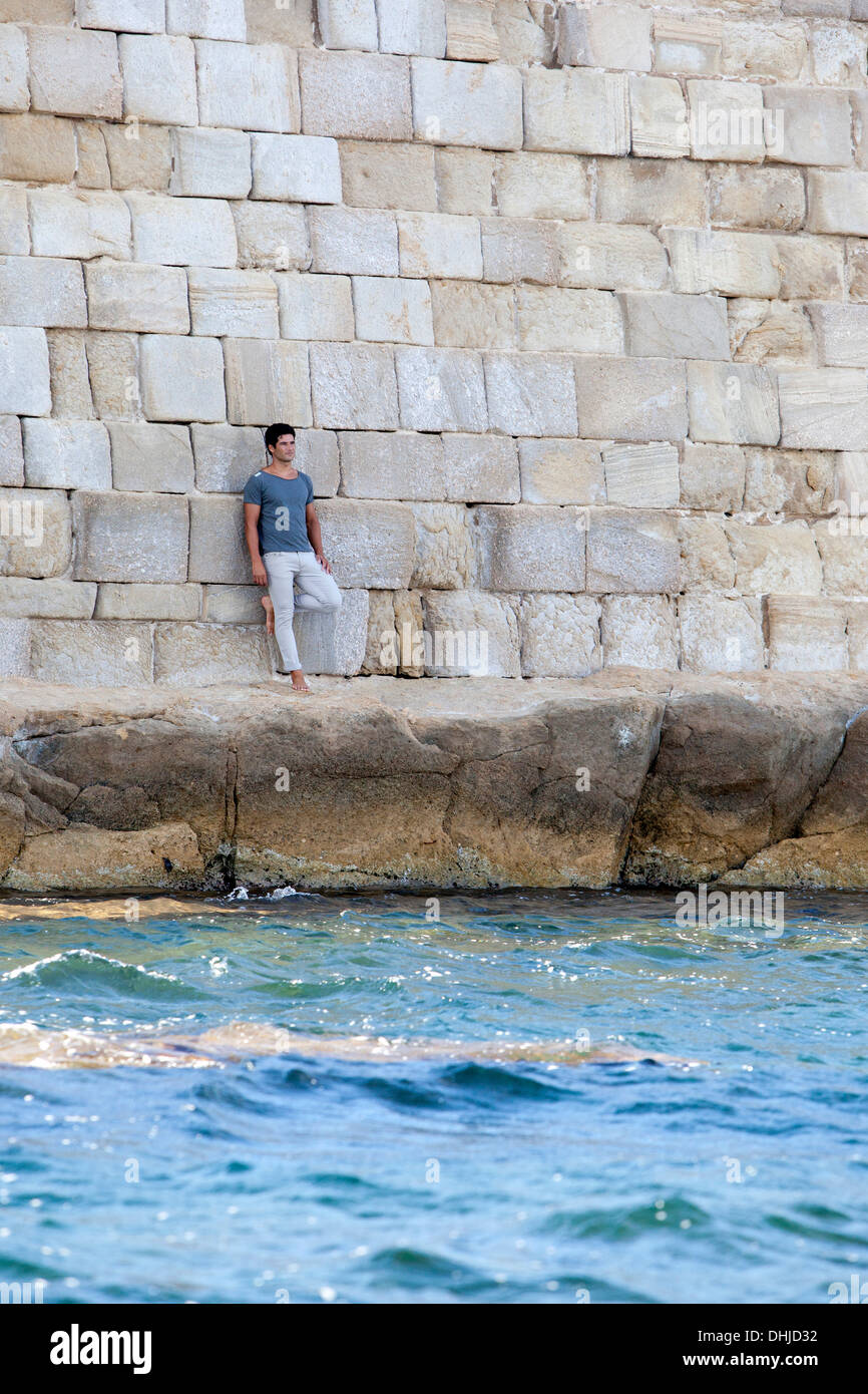 Young man leaning against a rock wall Stock Photo - Alamy