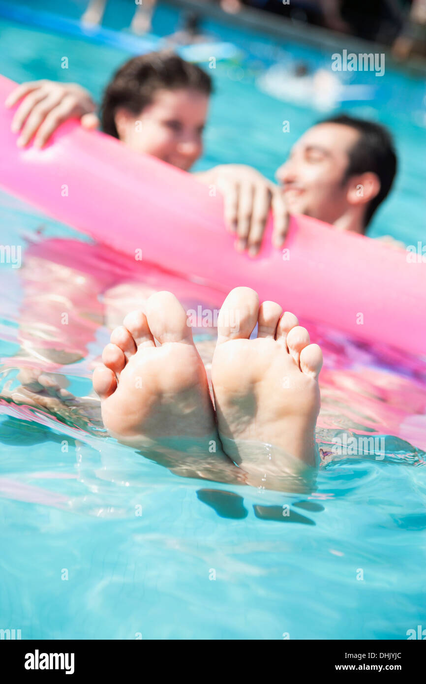 Two friends in a pool holding onto an inflatable raft with feet ...