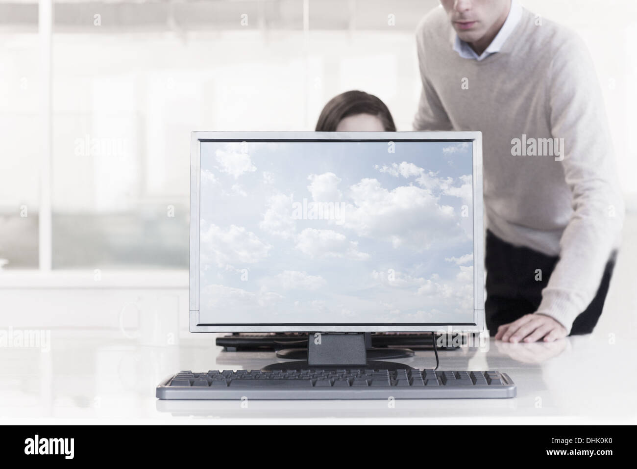 Two coworkers looking at a computer, computer monitor with clouds and ...