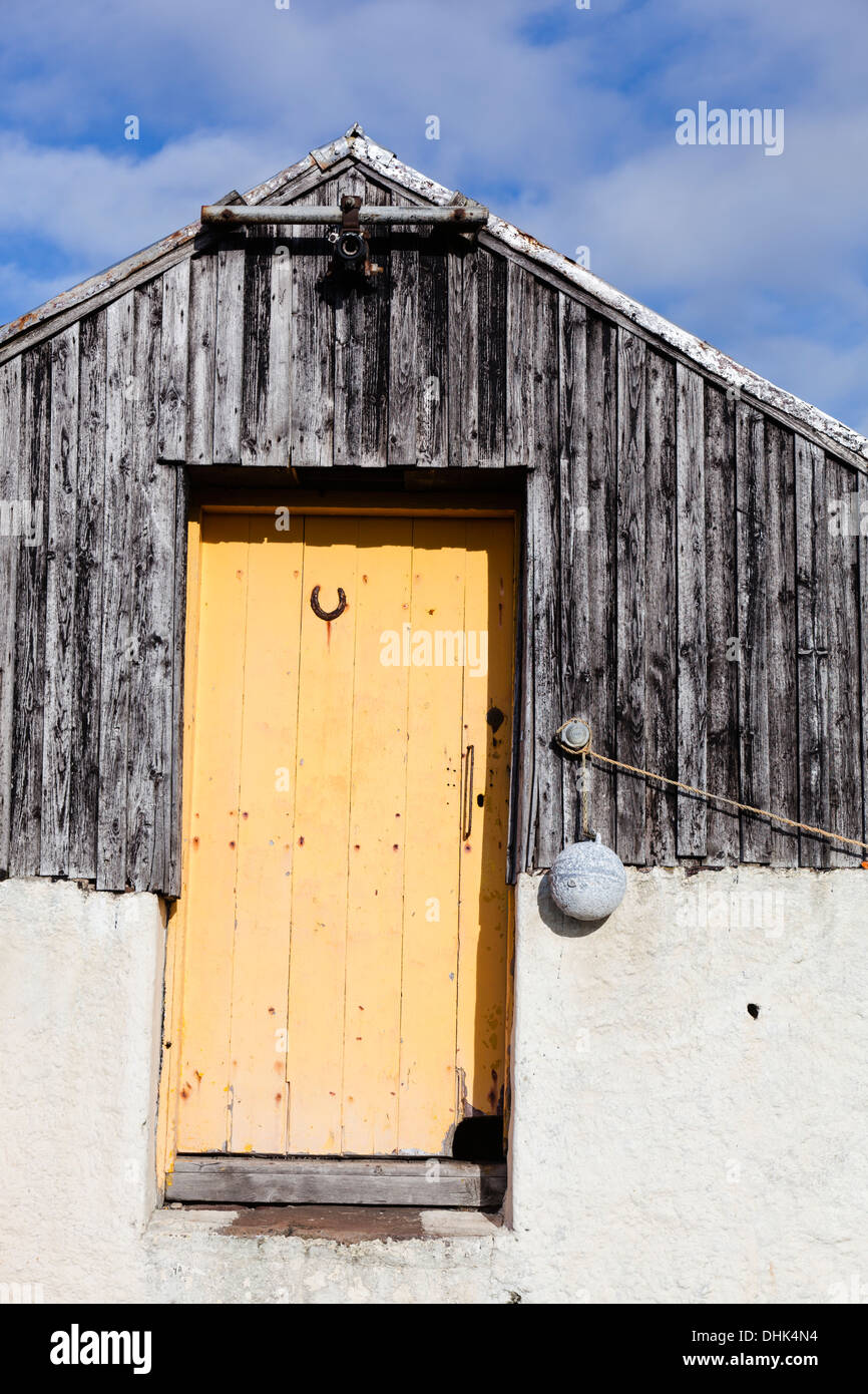 Old hut with a bright yellow wooden door and weathered wooden cladding ...
