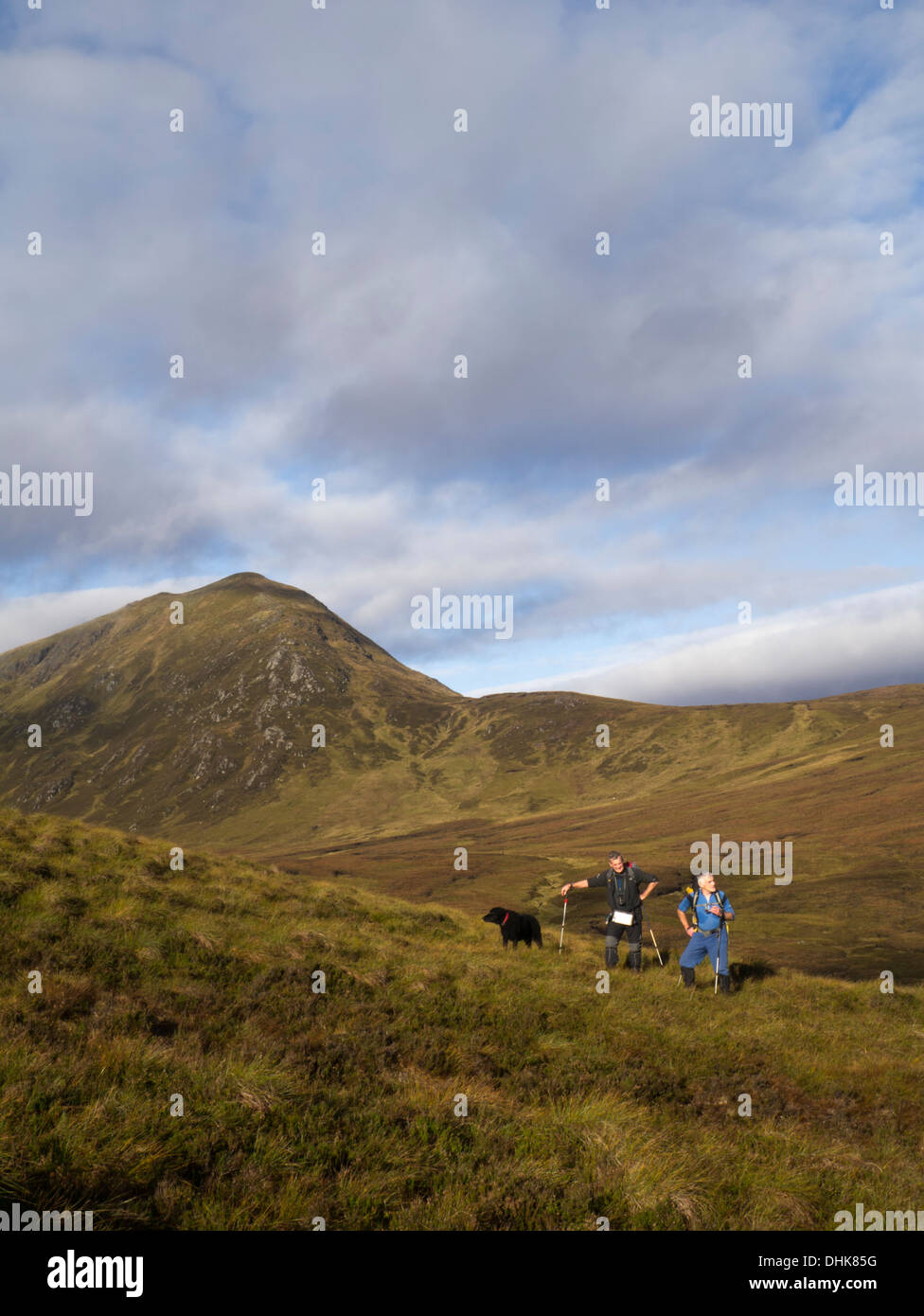 Two hikers and a dog ascending Meallan nan Uan. Sgurr a' Mhuilin in the ...