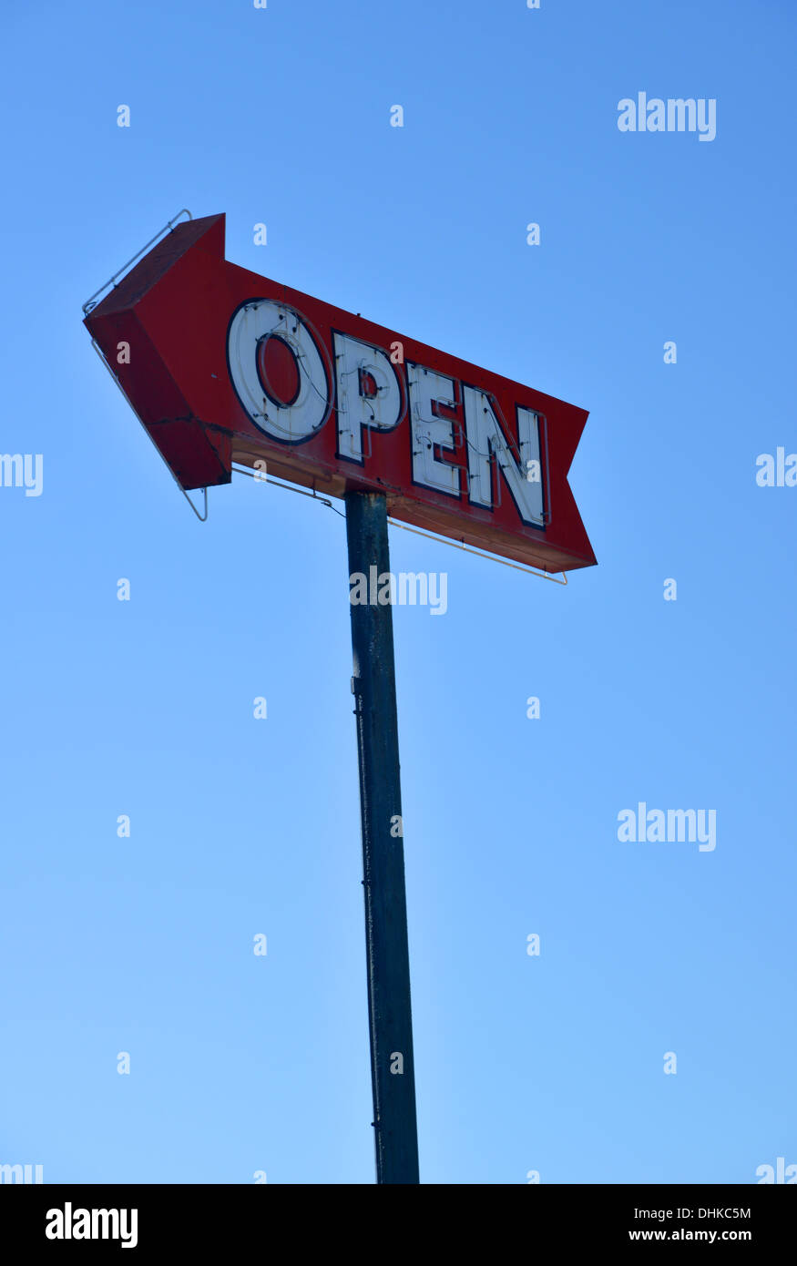 Old neon Open sign shaped like an arrow, red and faded against a blue ...