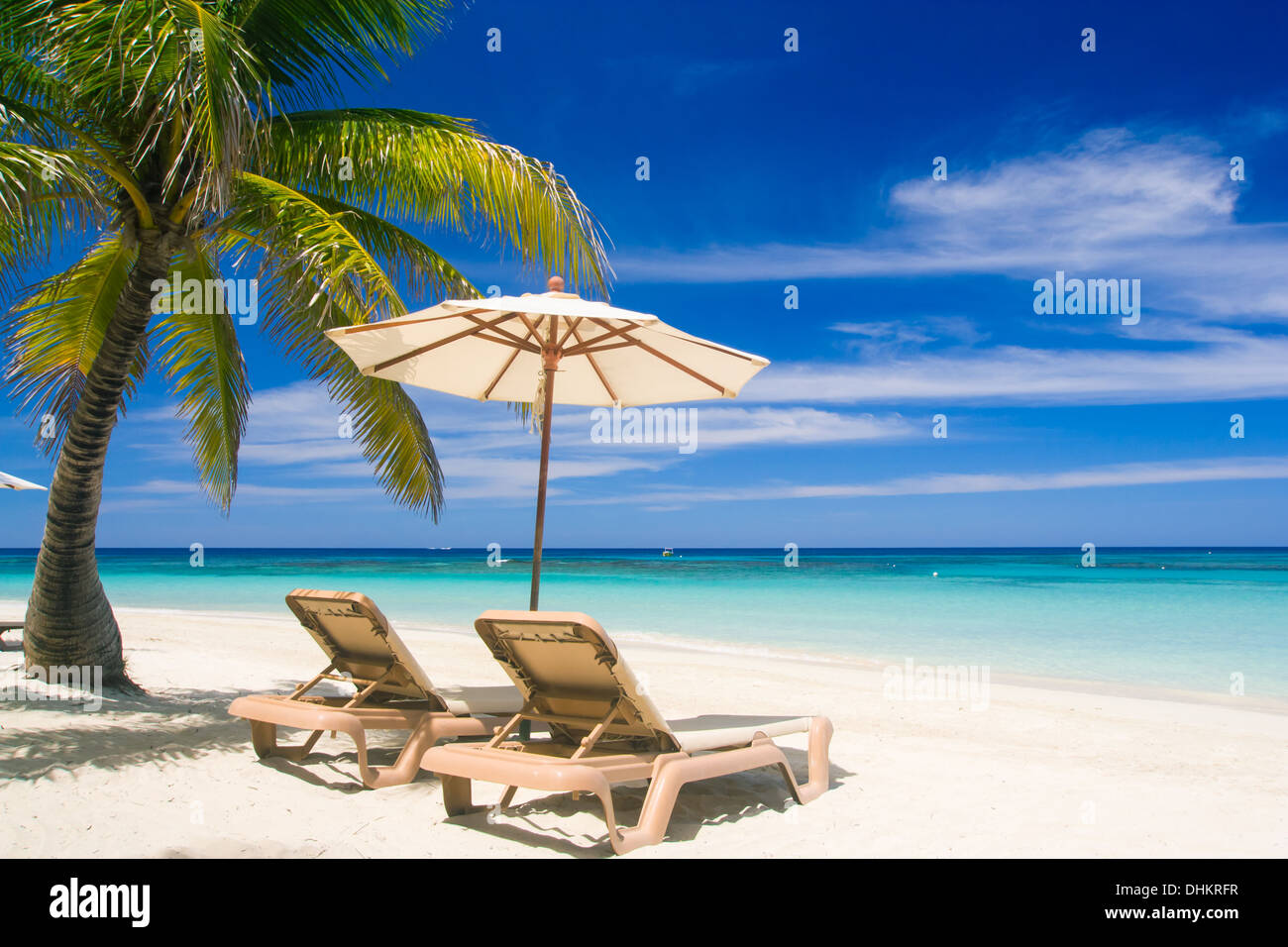 Beach charis under parasols framed by palm frond. Roatan, Honduras ...