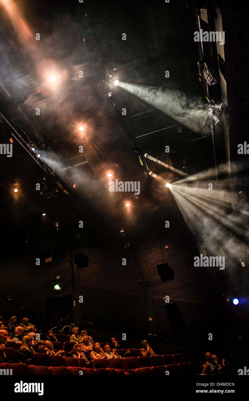 A theatre audience, watching a play, with dramatic lighting beams ...