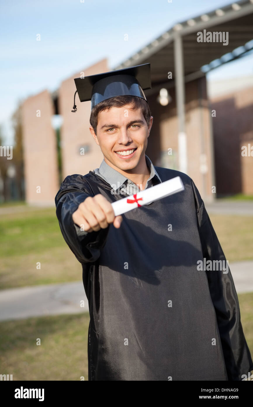 Man In Graduation Gown Showing Diploma On University Campus Stock Photo ...
