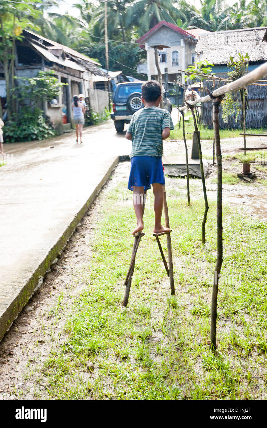 A young boy plays with some stilts outside his home on the island of ...