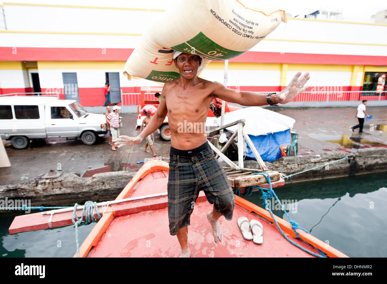 A man balances a heavy load as he loads a boats at a wharf at Tacloban ...