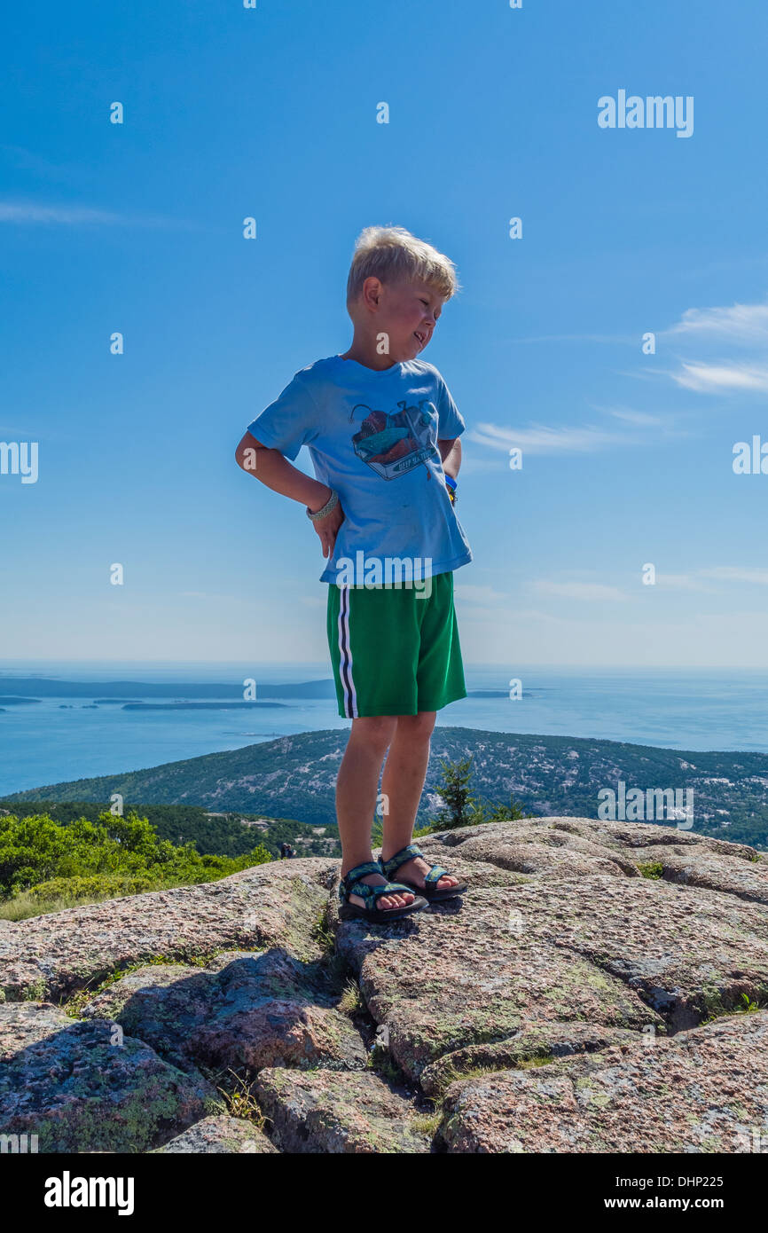 A blond haired boy stands on a large rock formation with his hands on ...