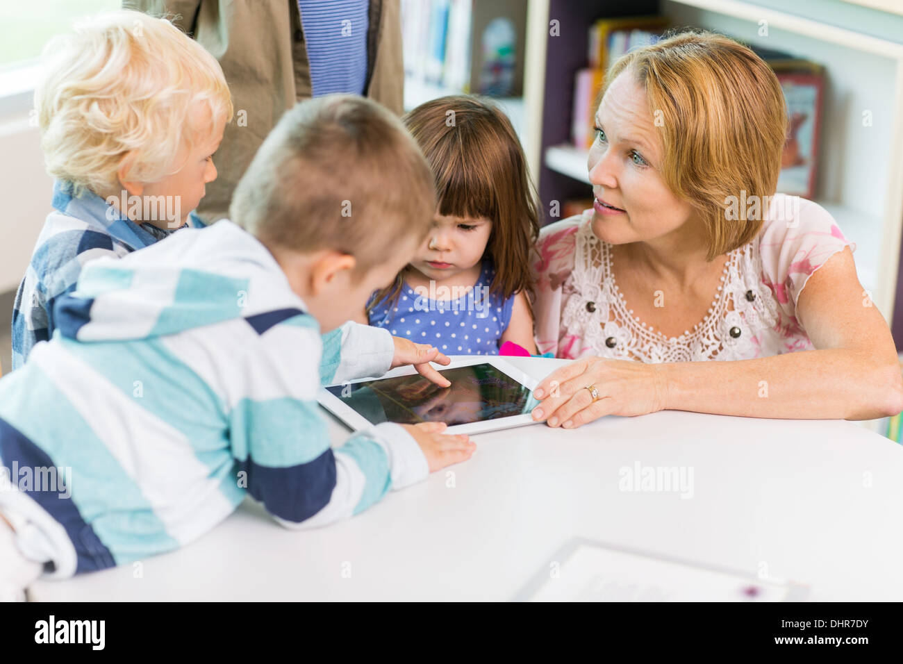 Teacher With Students Using Digital Tablet In Library Stock Photo - Alamy