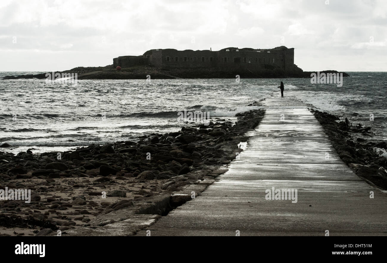 Man fishing on flooded causeway at Fort Ile de Raz, Alderney, Channel ...