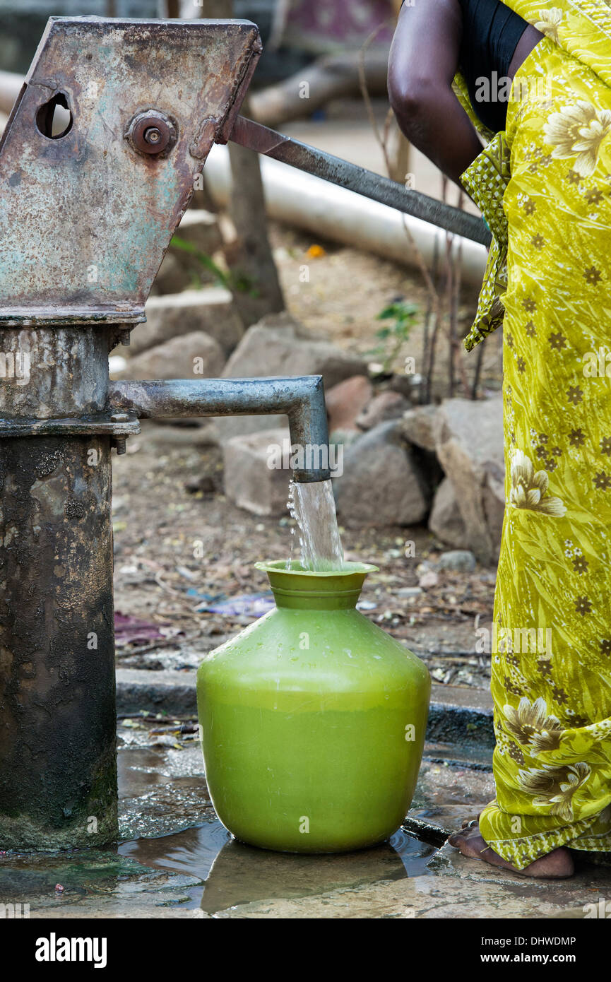 Rural indian woman filling plastic water pot from a rural hand pump ...