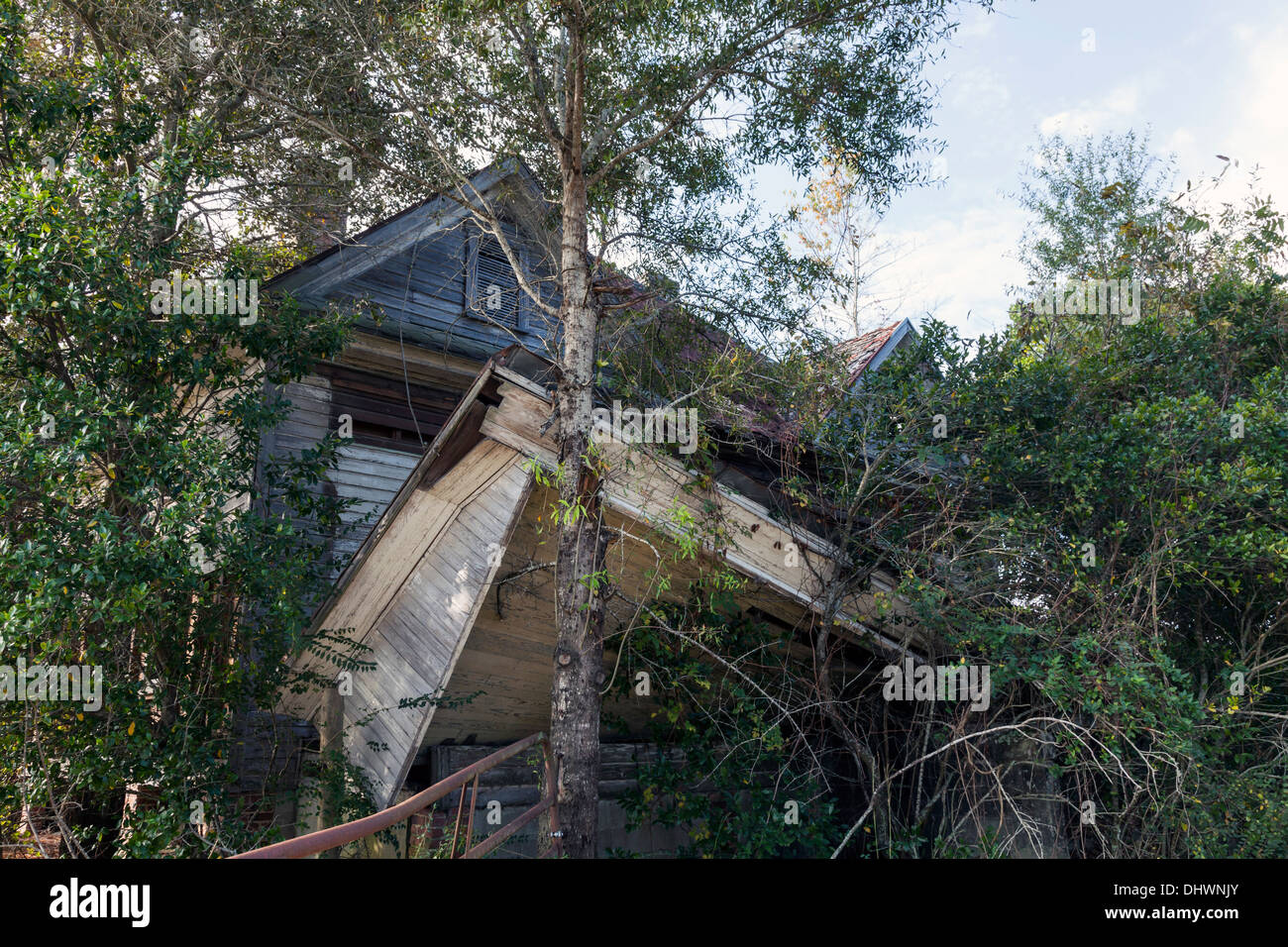 Overgrown and abandoned farmhouse with collapsed porch roof alongside I ...