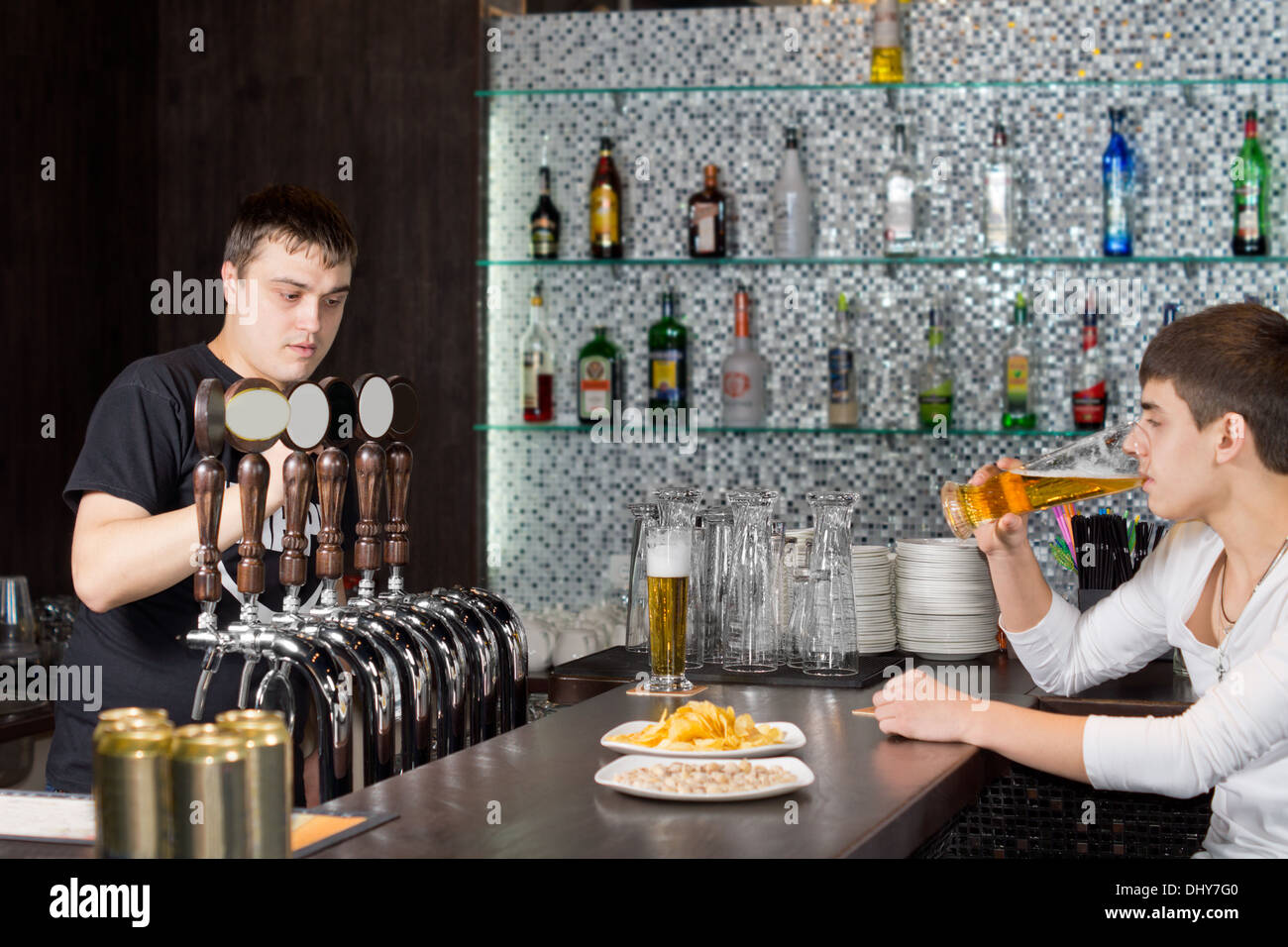 Barman working dispensing draught beer while a young male customer ...