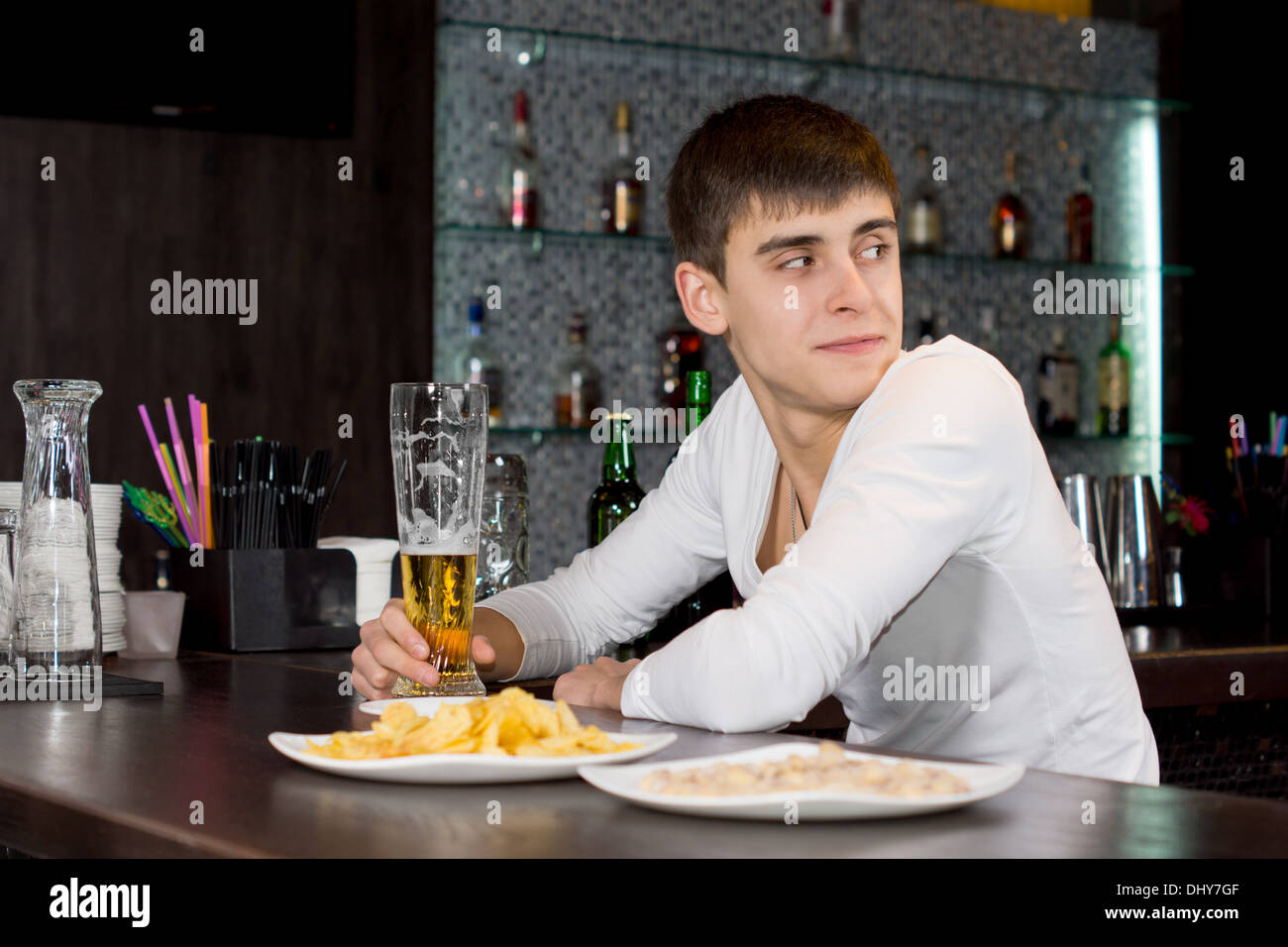 Young man sitting at a bar counter with a half drunk pint of beer ...