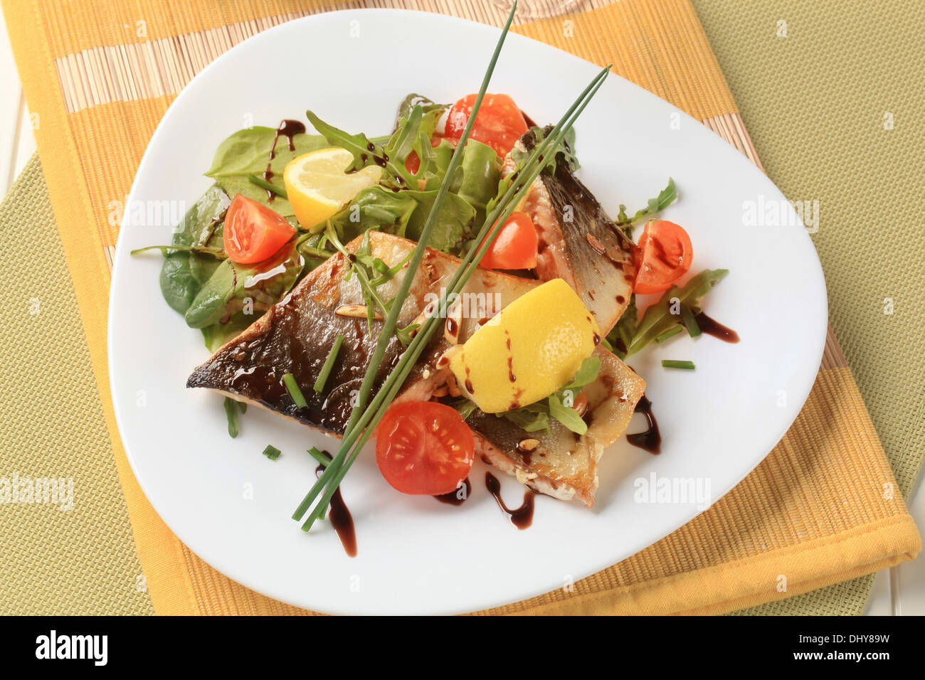 Portioned fish fillet on bed of salad greens drizzled with balsamic ...
