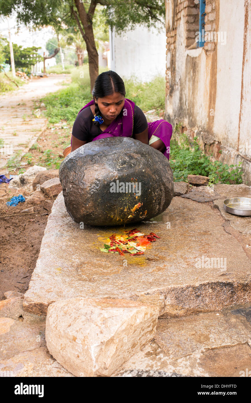 Indian woman using a stone to grind ingredients to make chutney outside ...