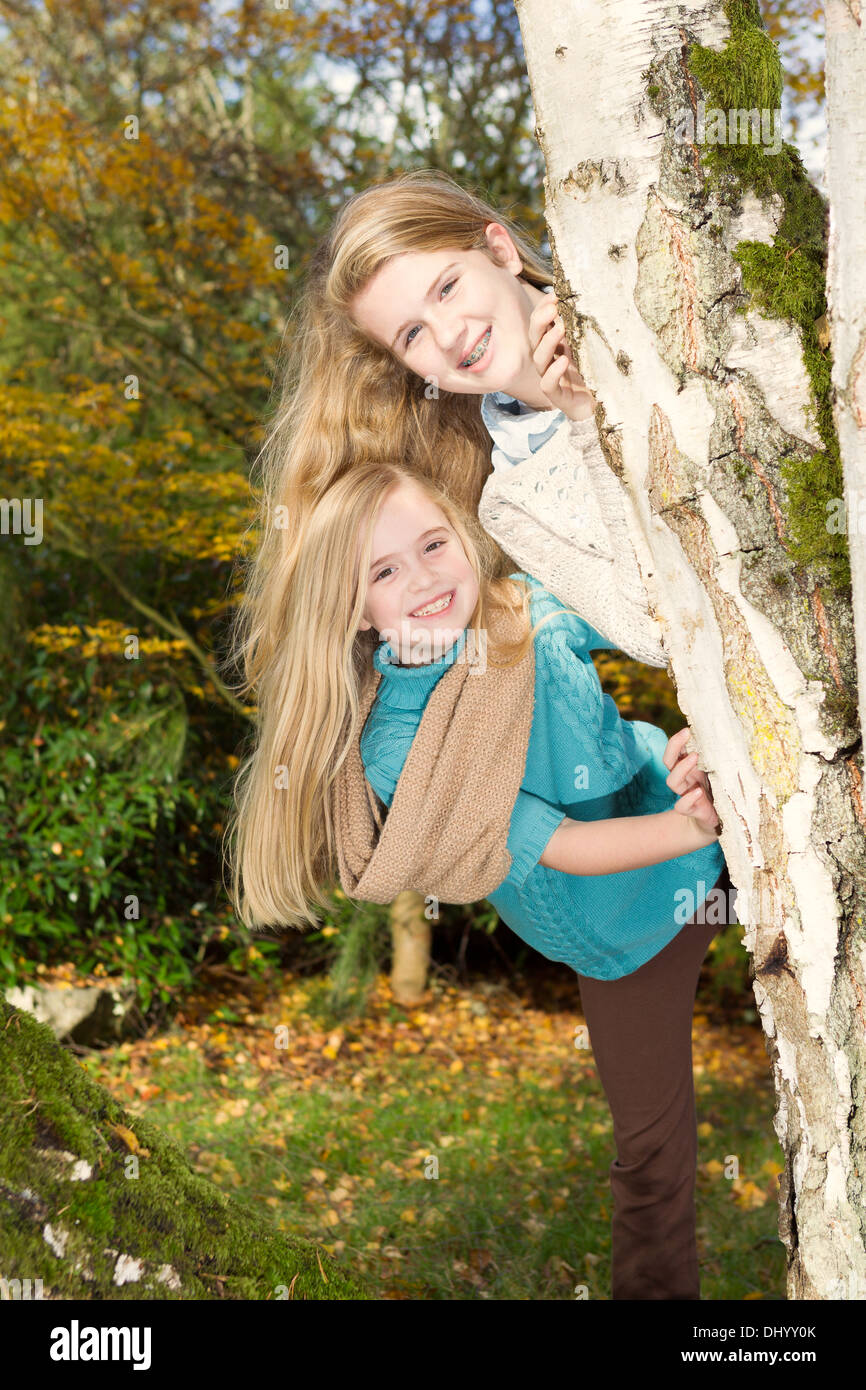 Vertical photo of young girls peeking from around tree with autumn ...