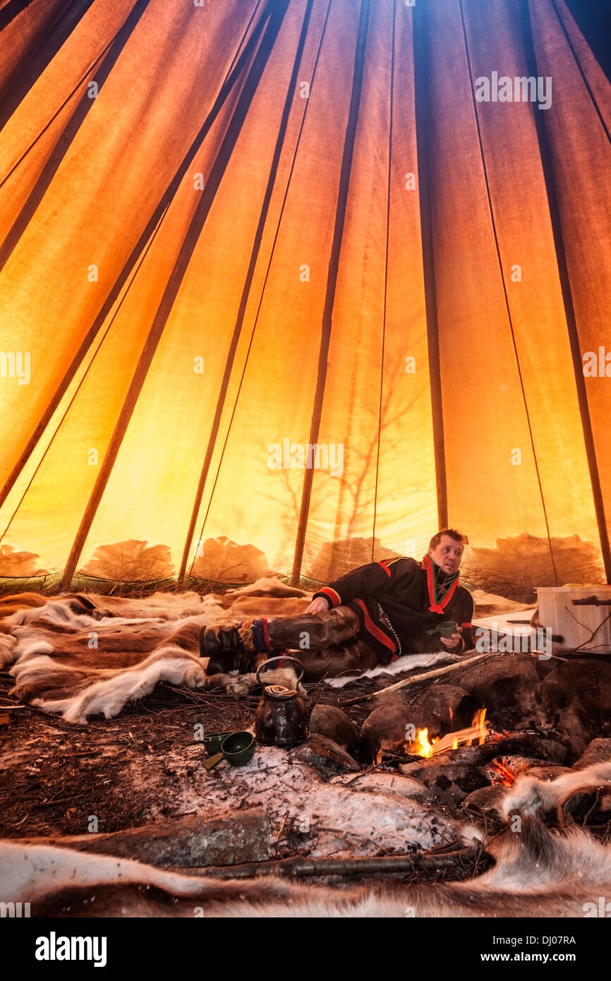 Sami man resting on reindeer fur skins inside his lavvu Sami tent in ...