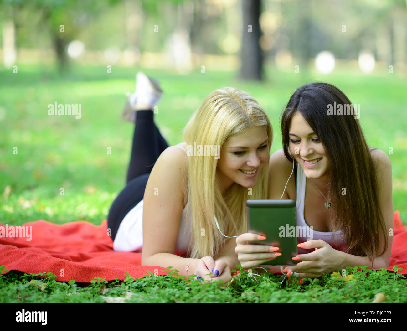 Teenage girls having fun online on digital tavblet outdoors in park ...
