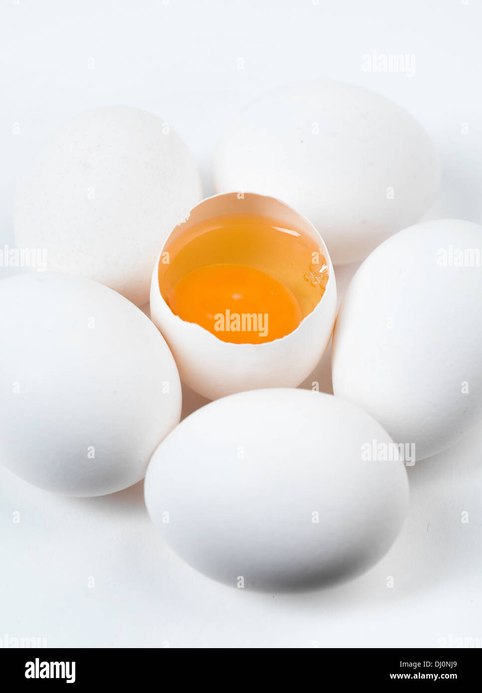 whole white chicken eggs surrounding one open egg, yolk exposed Stock ...