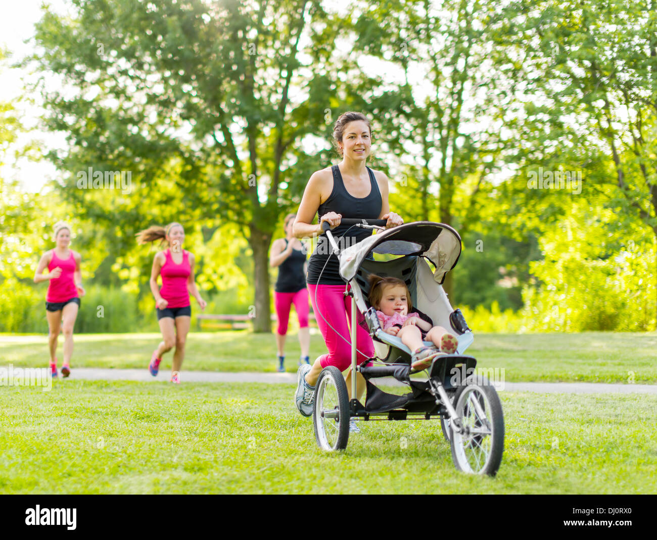 Woman pushing her little girl in a toddler while running in nature with ...