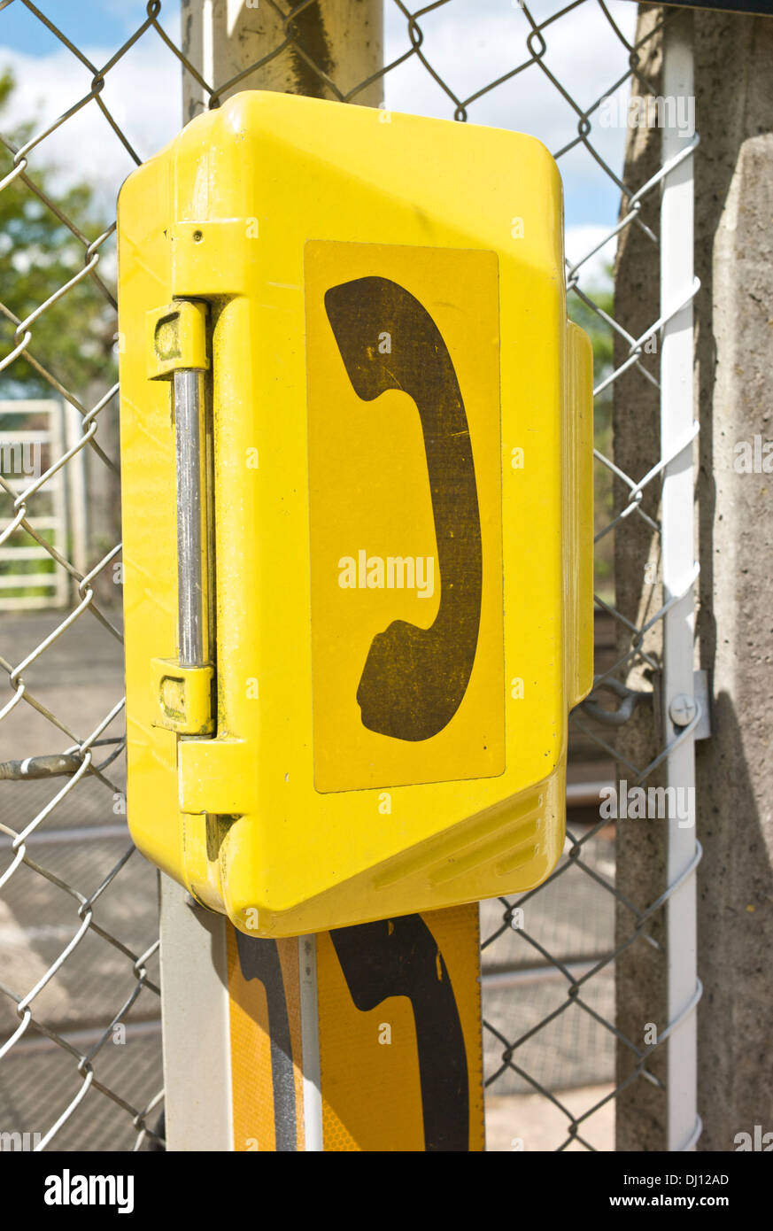 Yellow railway telephone box against wire mesh chainlink type fence ...