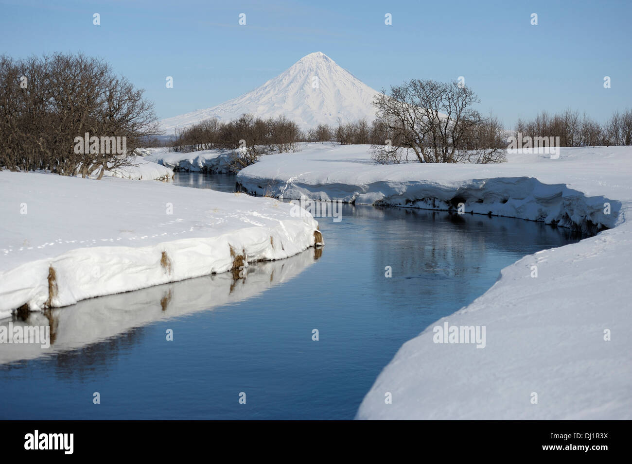 Tikhaya River flows through the snowy tundra. Kronotsky Volcano is in ...