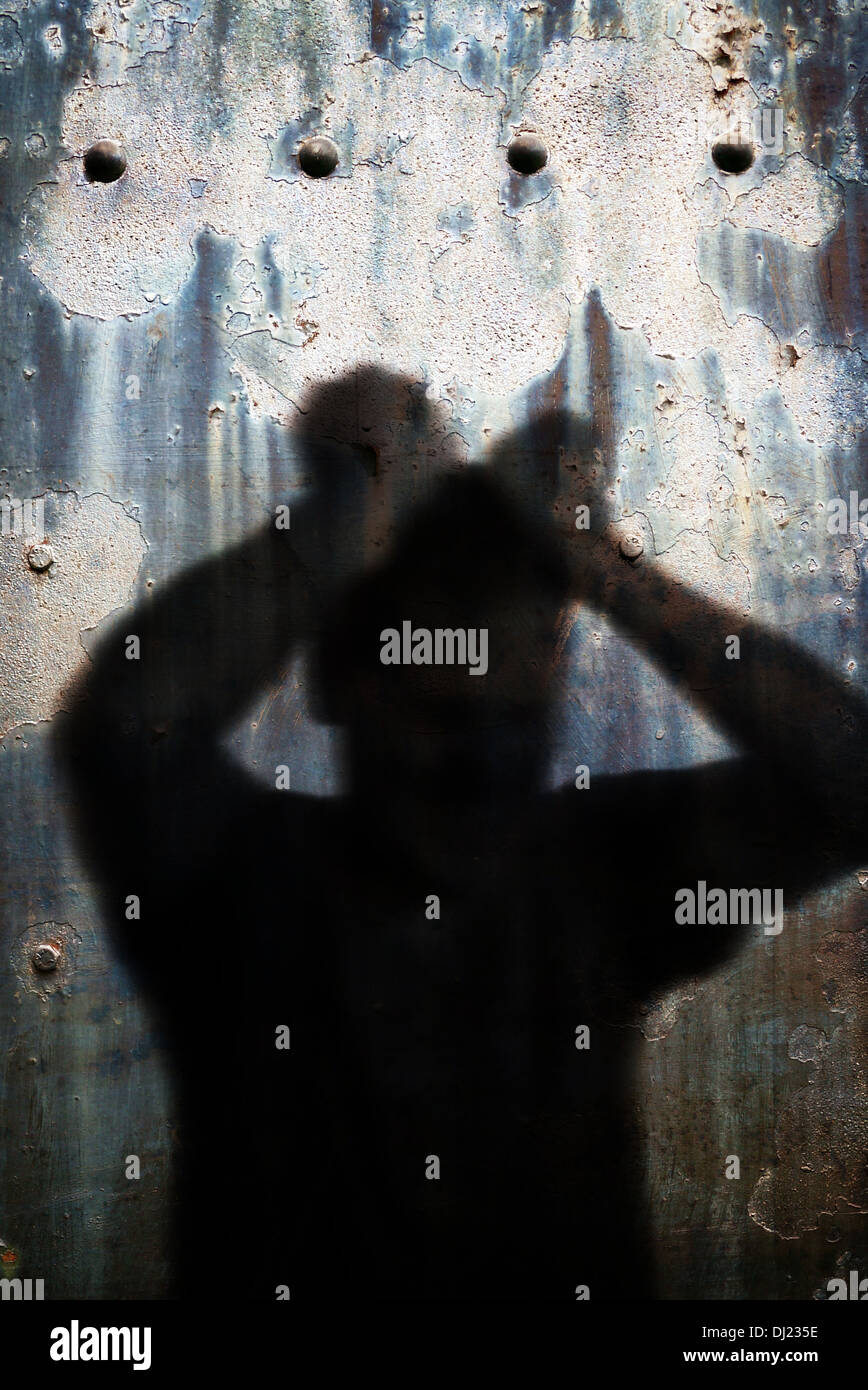 A man's shadow with hands on head against a rusty metal background ...