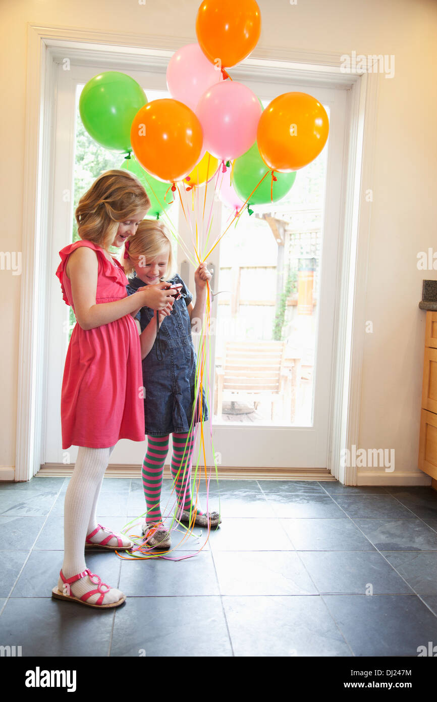 Two young girls standing inside a house with balloons while looking at ...