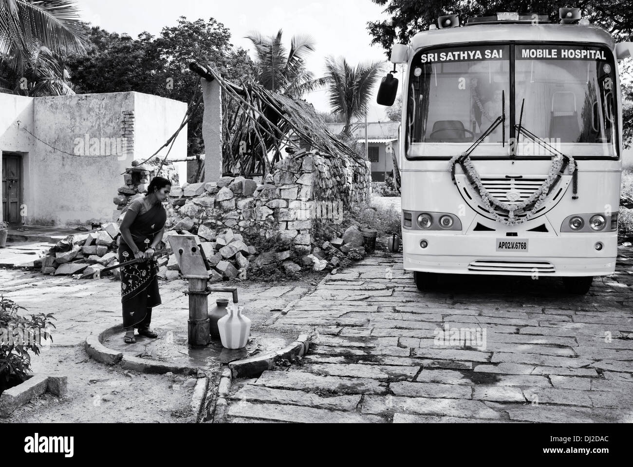 Indian village woman filling pot with water from a hand pump in front ...