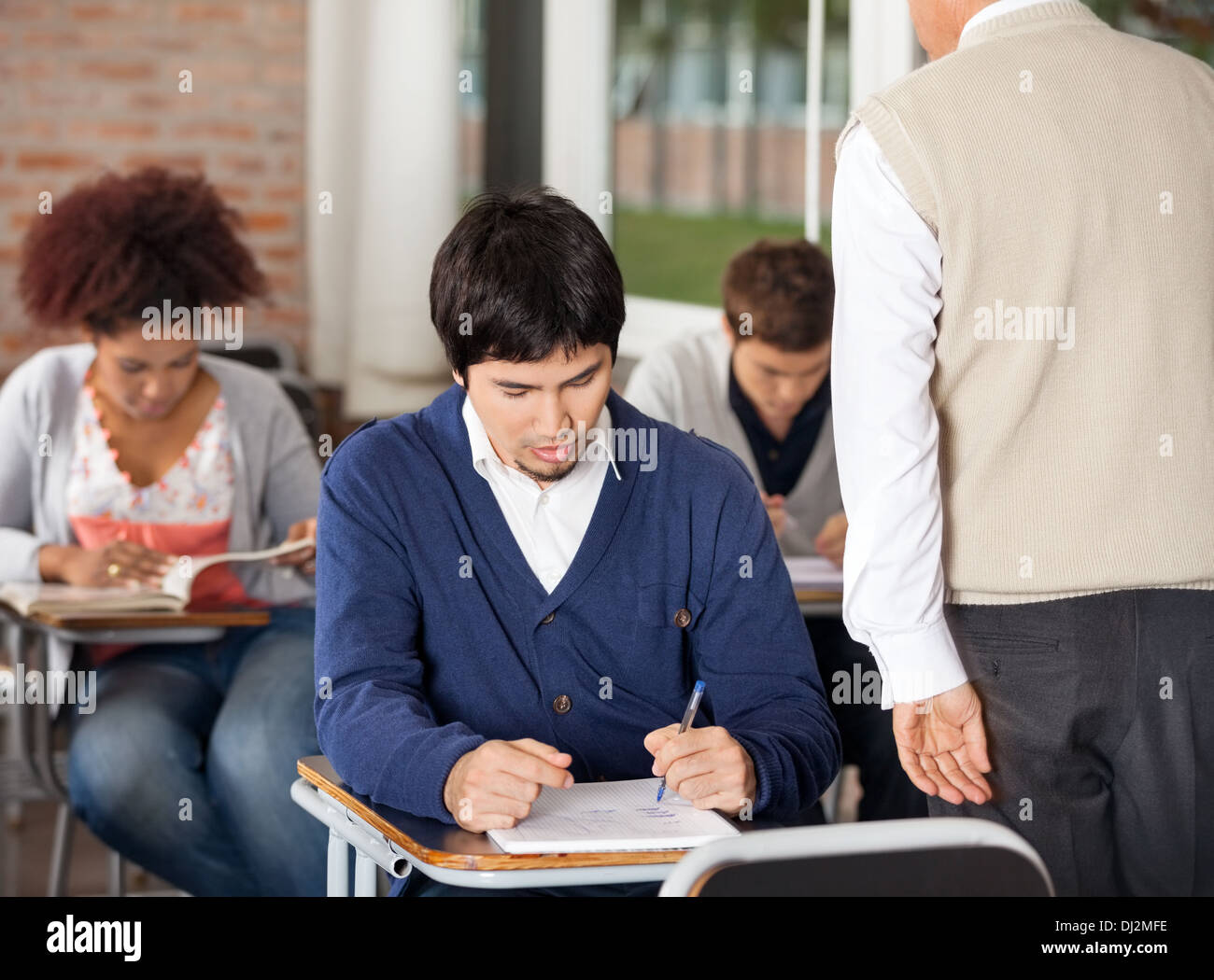 Students Giving Exam While Teacher Supervising Them In Classroom Stock ...