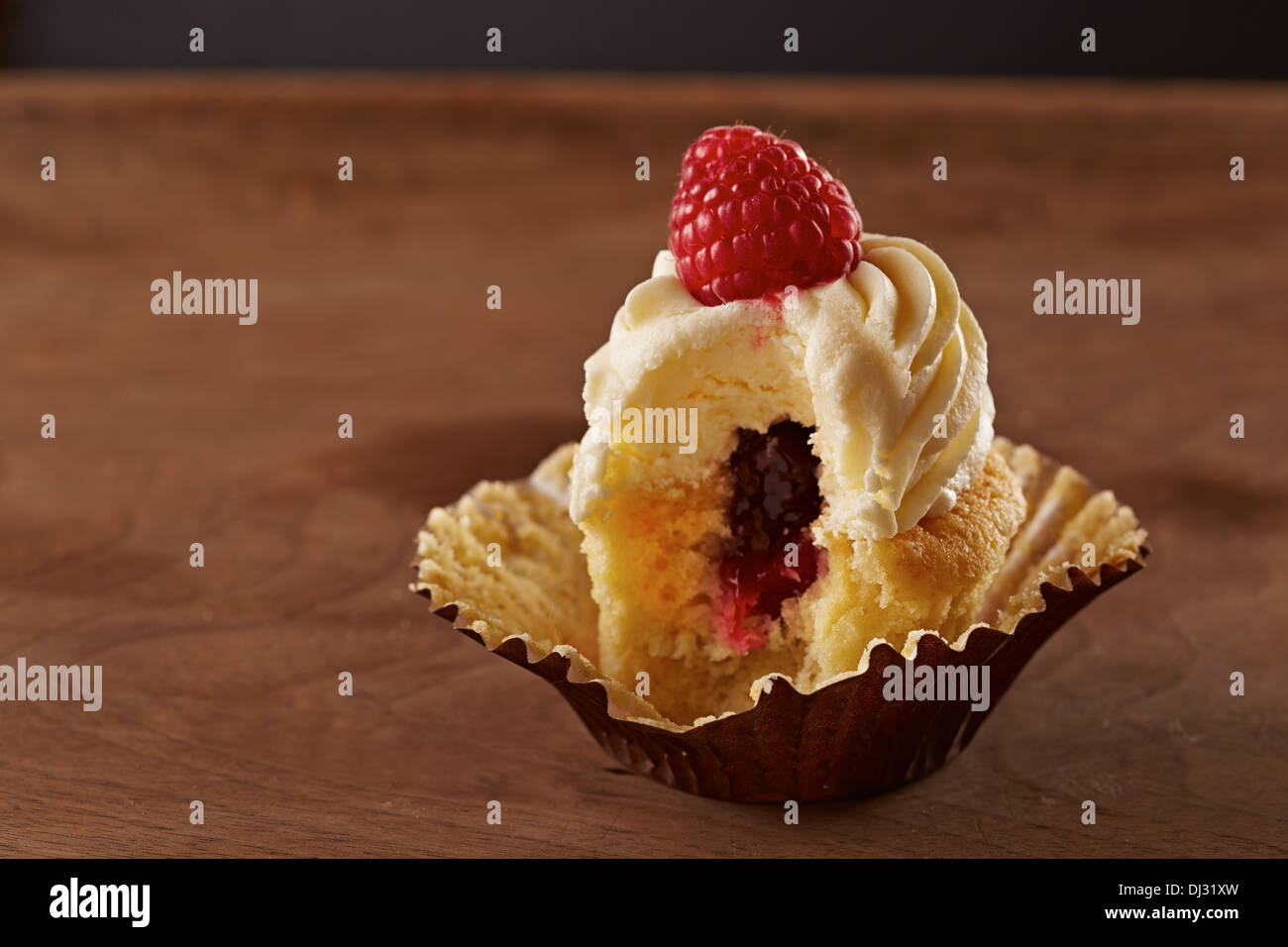 Bitten raspberry filled cupcake on wooden table and black background ...