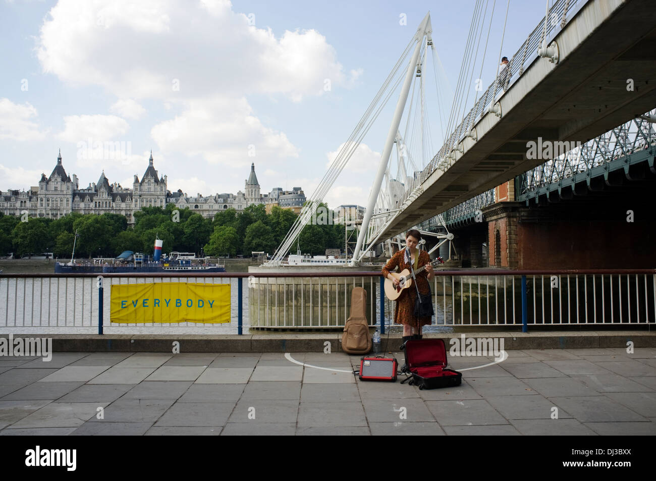 A young woman playing her guitar and singing, busking under the ...
