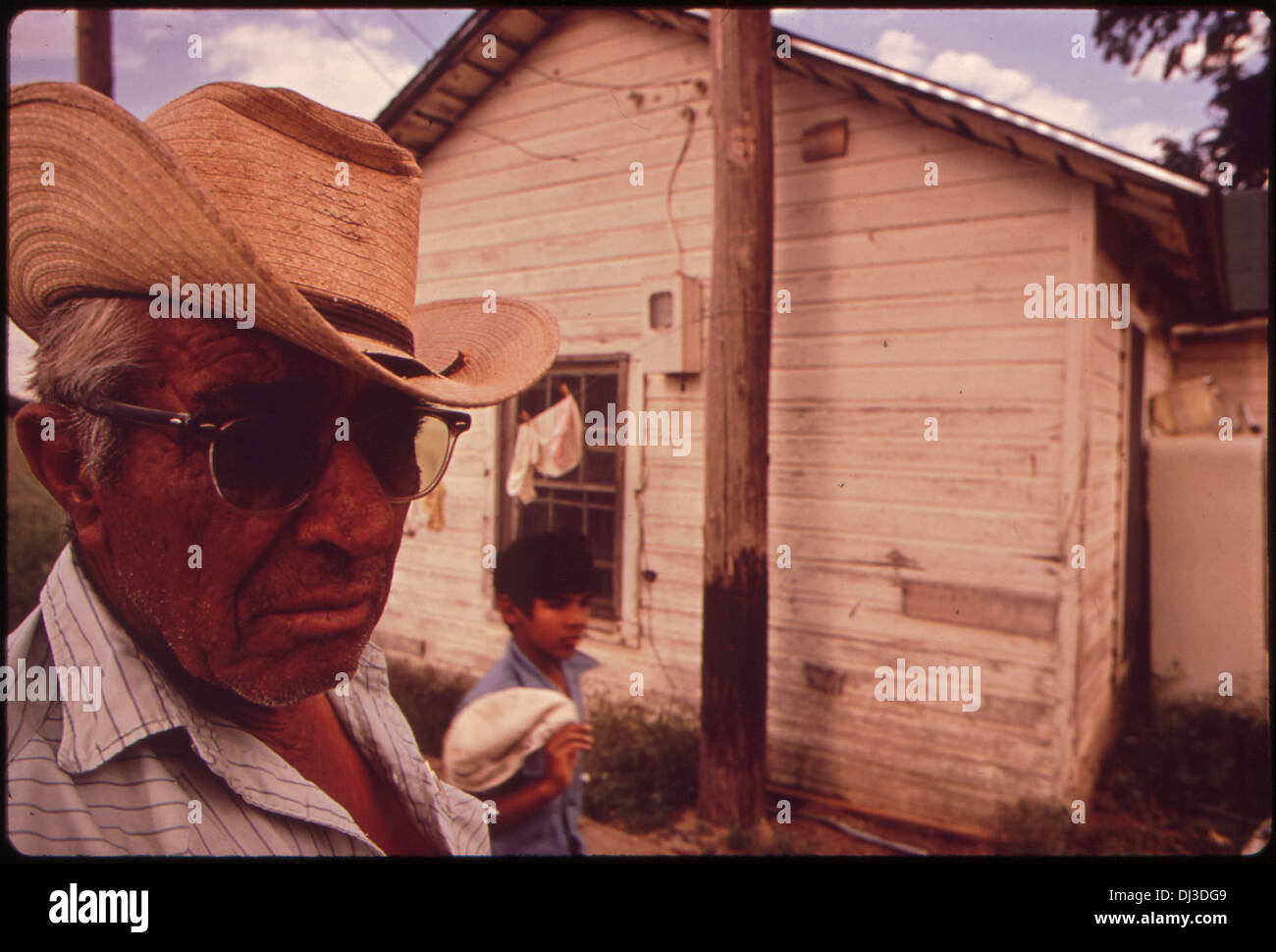 MIGRANT WORKER WITH HIS GRANDCHILDREN IN FRONT OF TWO ROOM SHACK WHICH ...