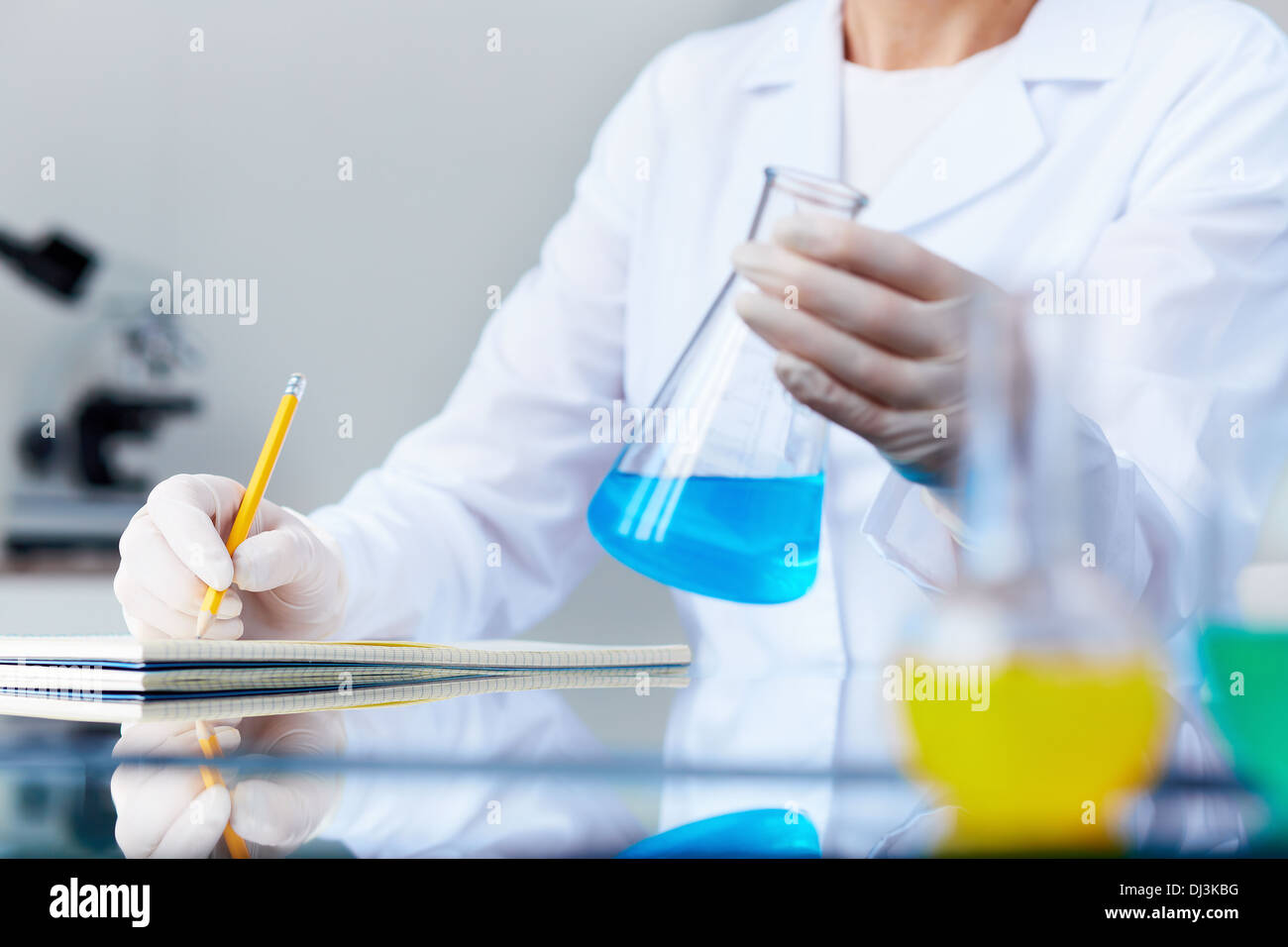 Hand of chemist with pencil writing down observations in laboratory ...