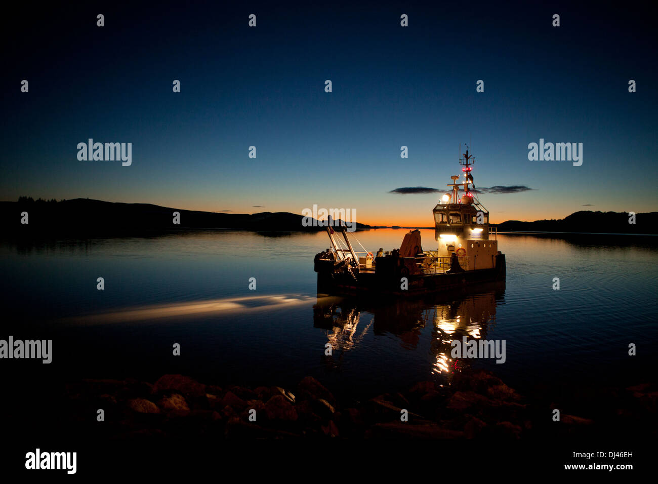A Tug boat shines a searchlight on the still Loch waters in the dying ...