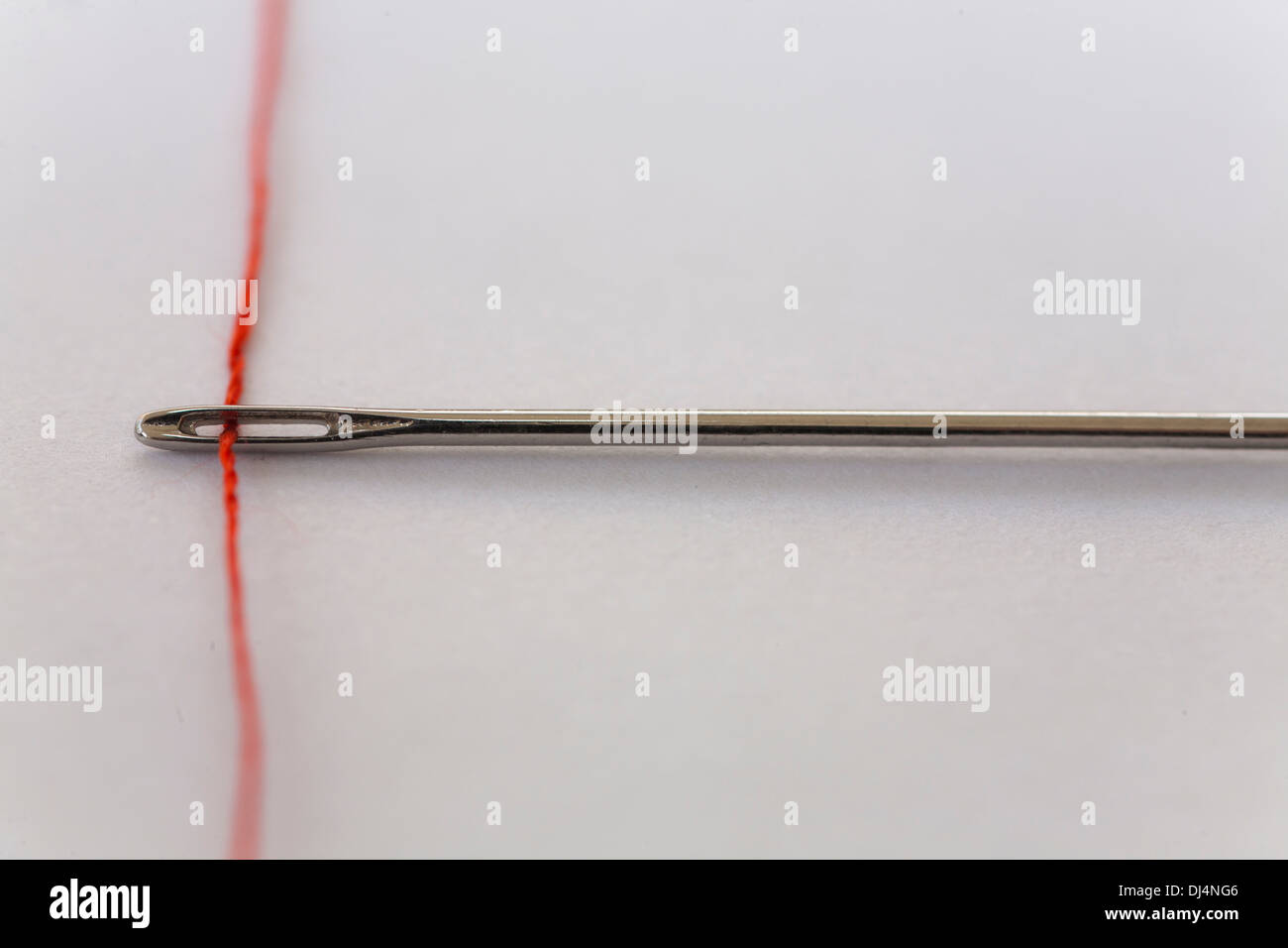 A vertical needle with red thread on a white background Stock Photo - Alamy