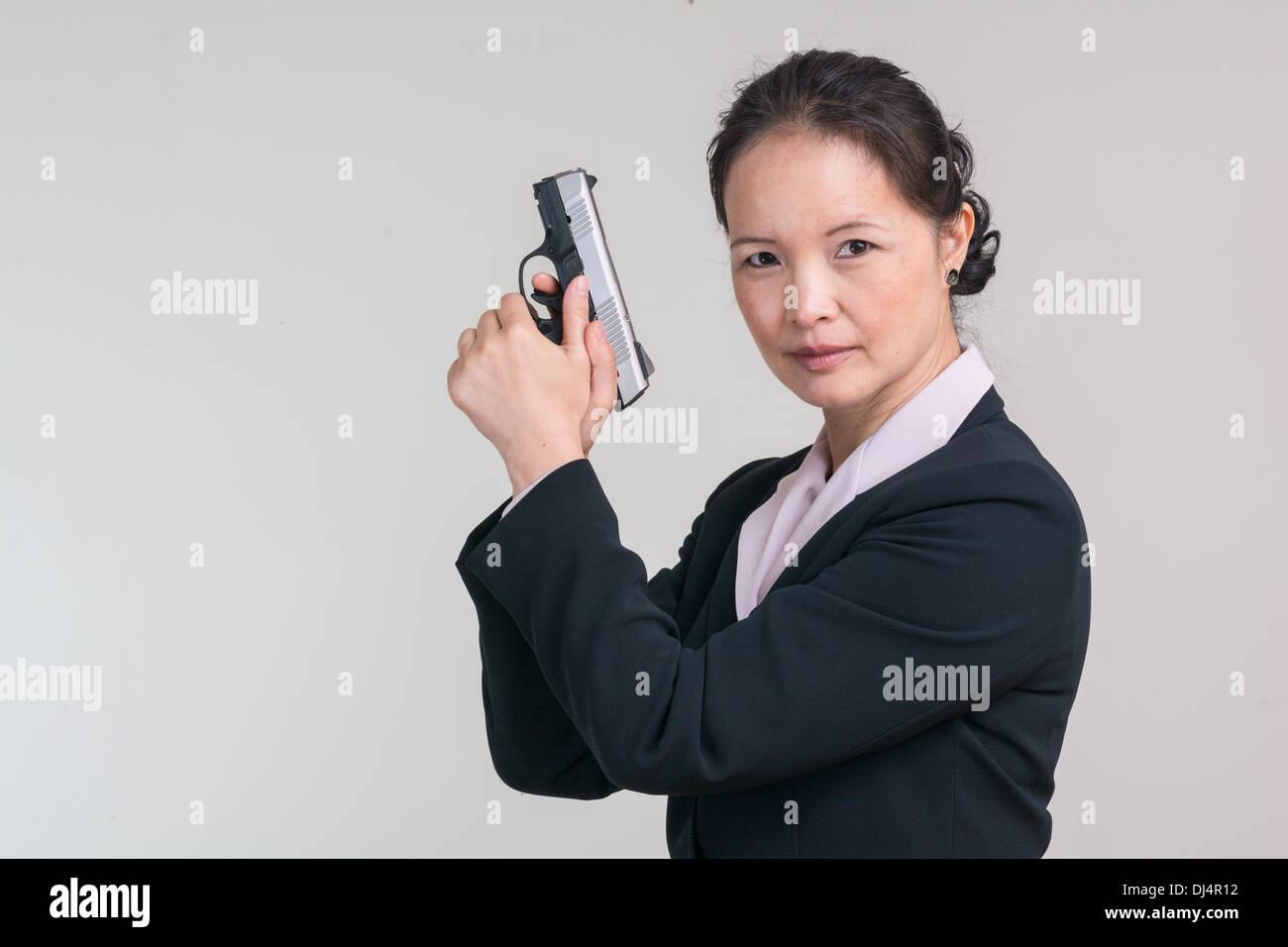 Portrait of woman in business suit holding a hand gun with agent pose ...