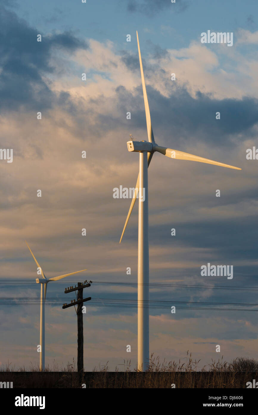 Two wind turbines and an old power line pole and wires after sunrise ...
