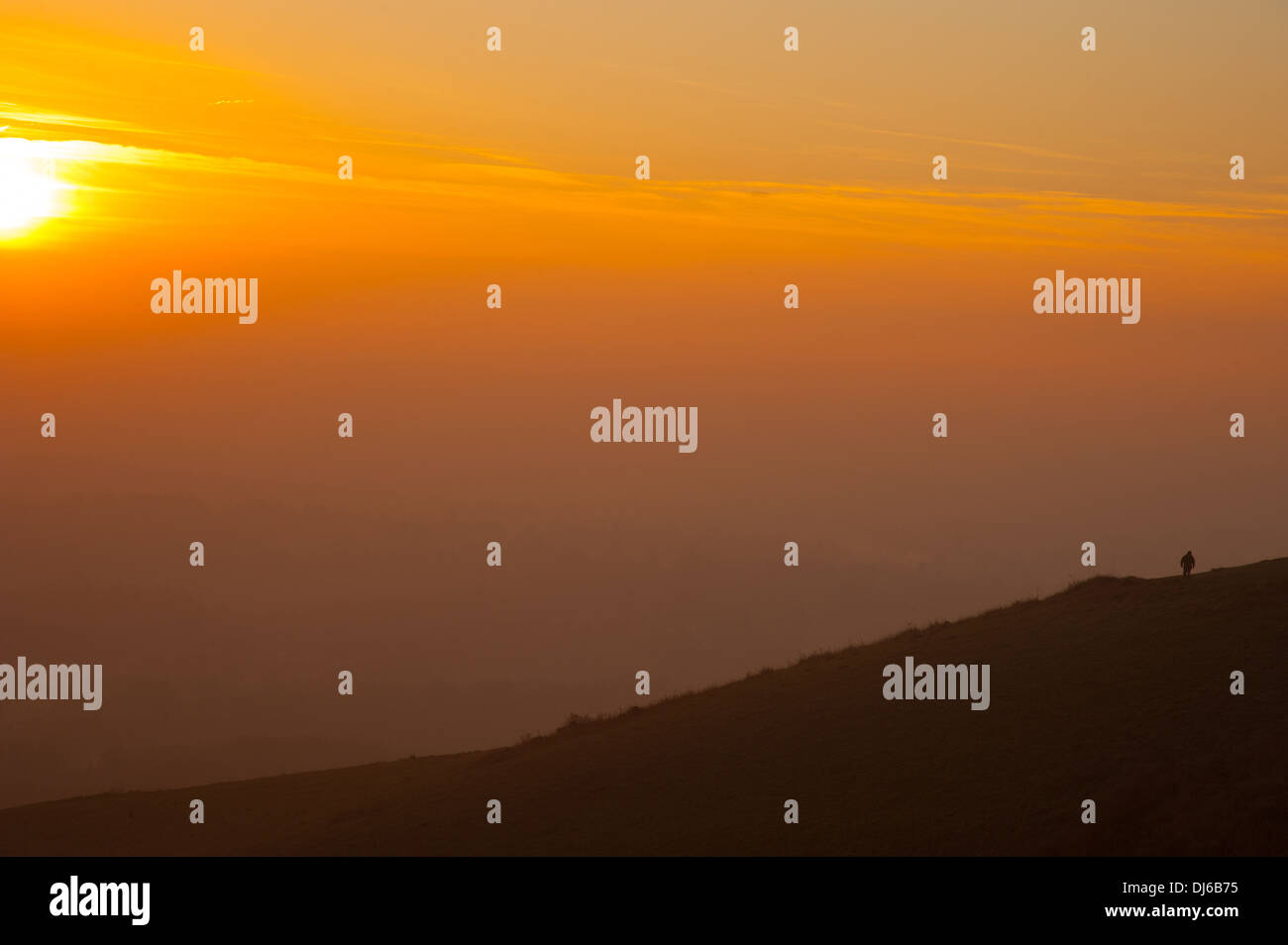 a hiker walking at the summit of a hill with a bright sunset. Colley ...