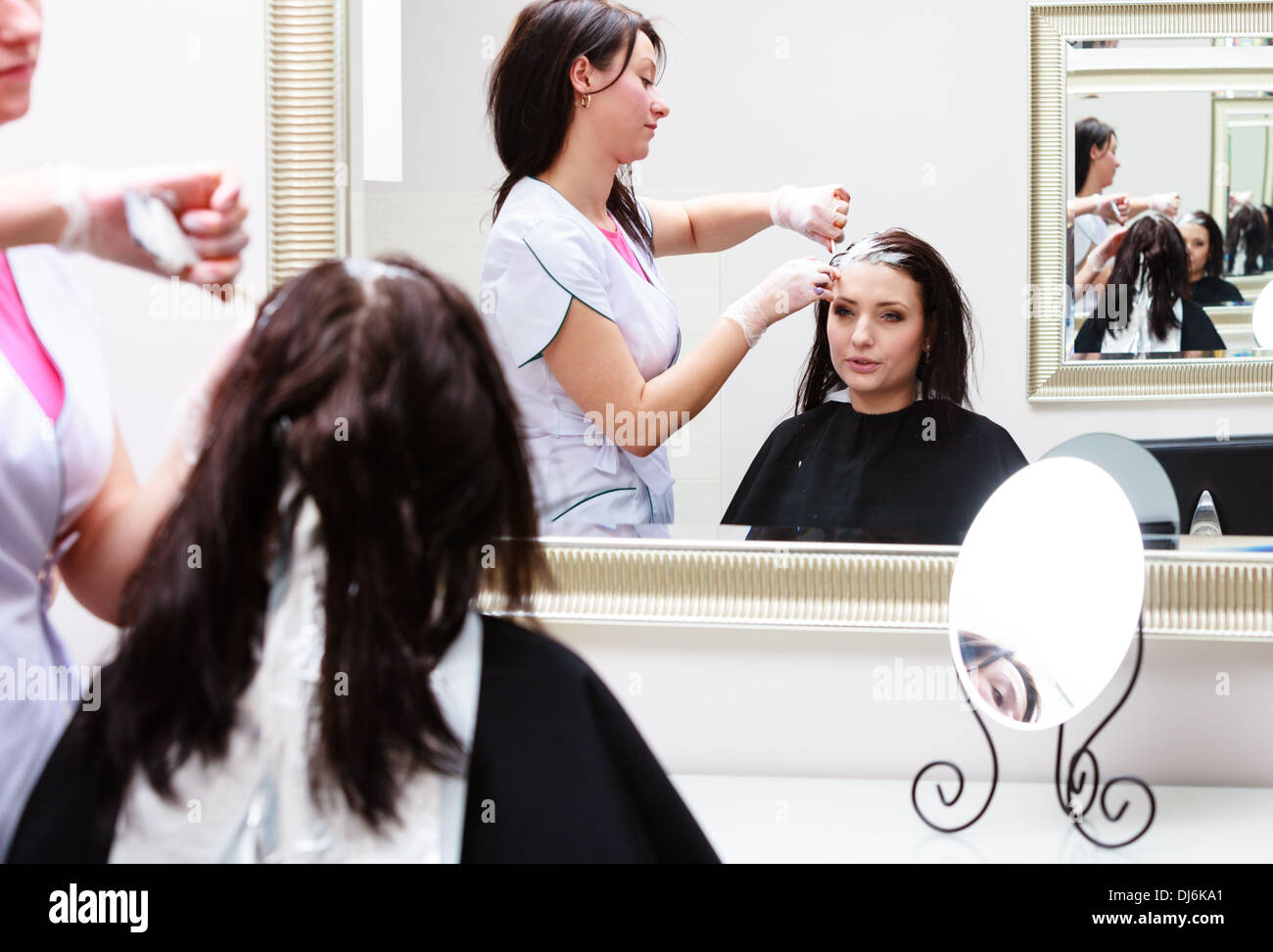 Hairdresser applying color to female customer at hair salon. Woman ...